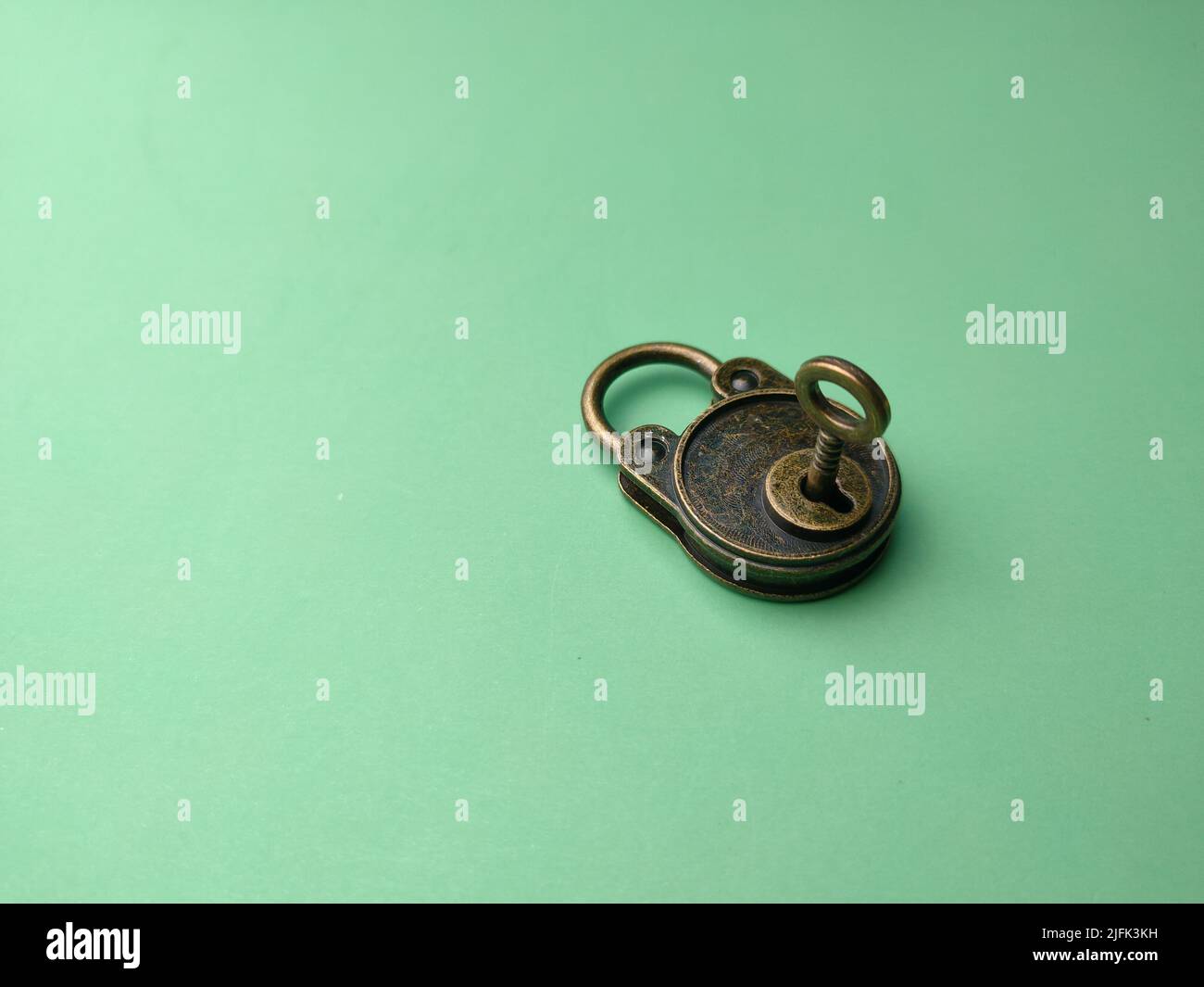 A bronze vintage padlock and a key on soft green paper background with ...