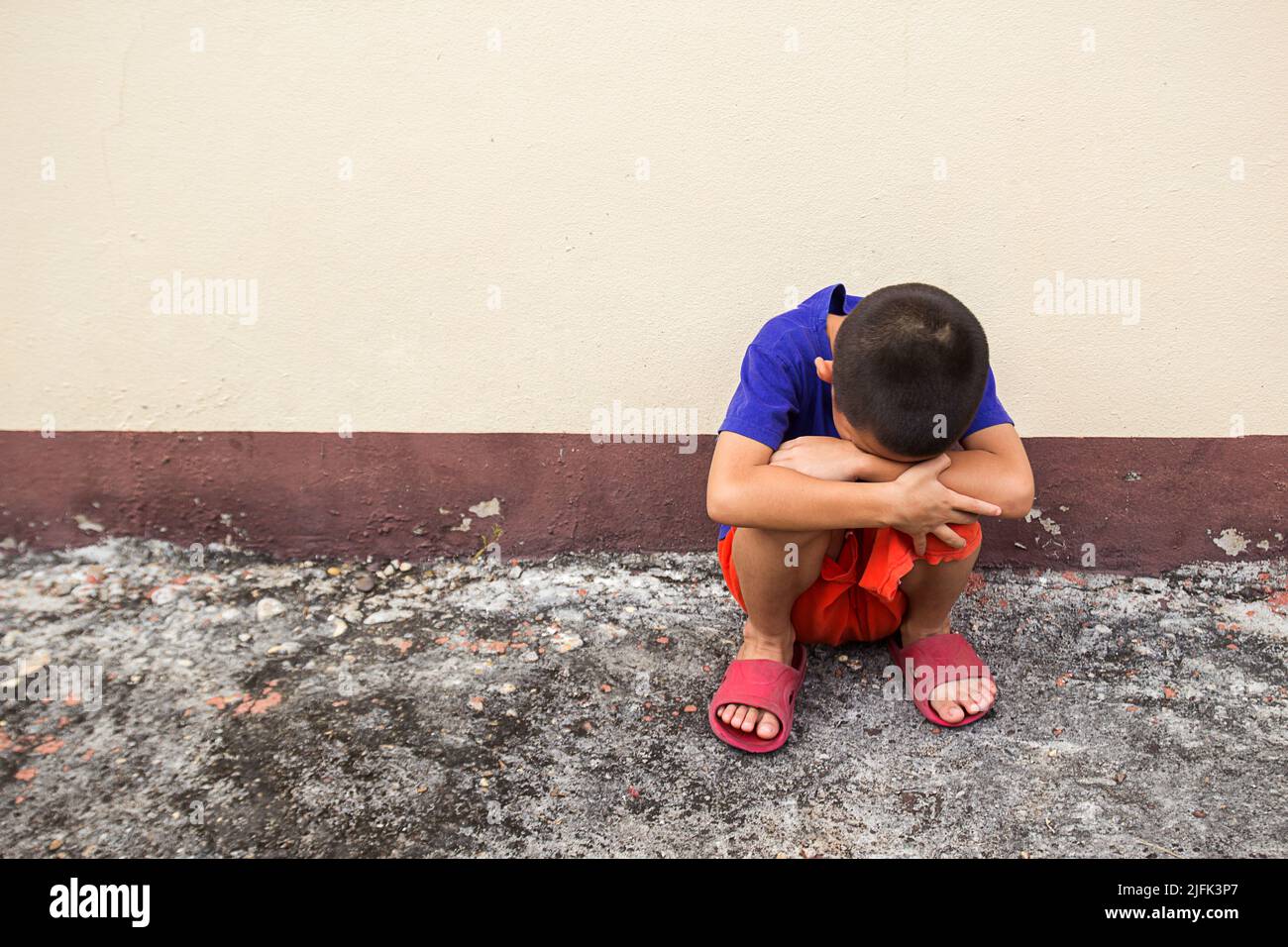 Sad little boy sitting on floor in empty room.taken with copy space ...
