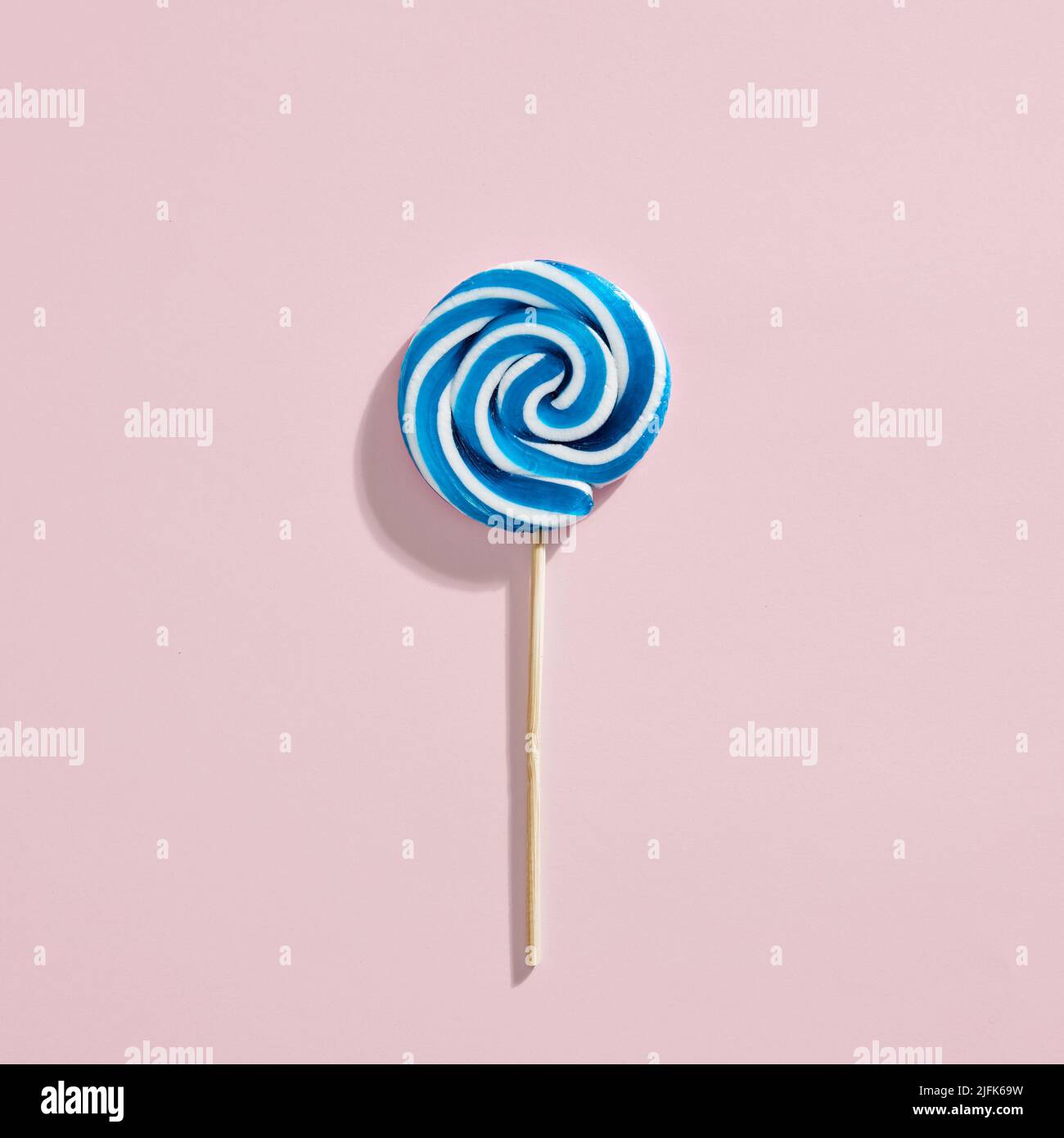 Blue and white colored swirl round candy lollipop on pink background ...