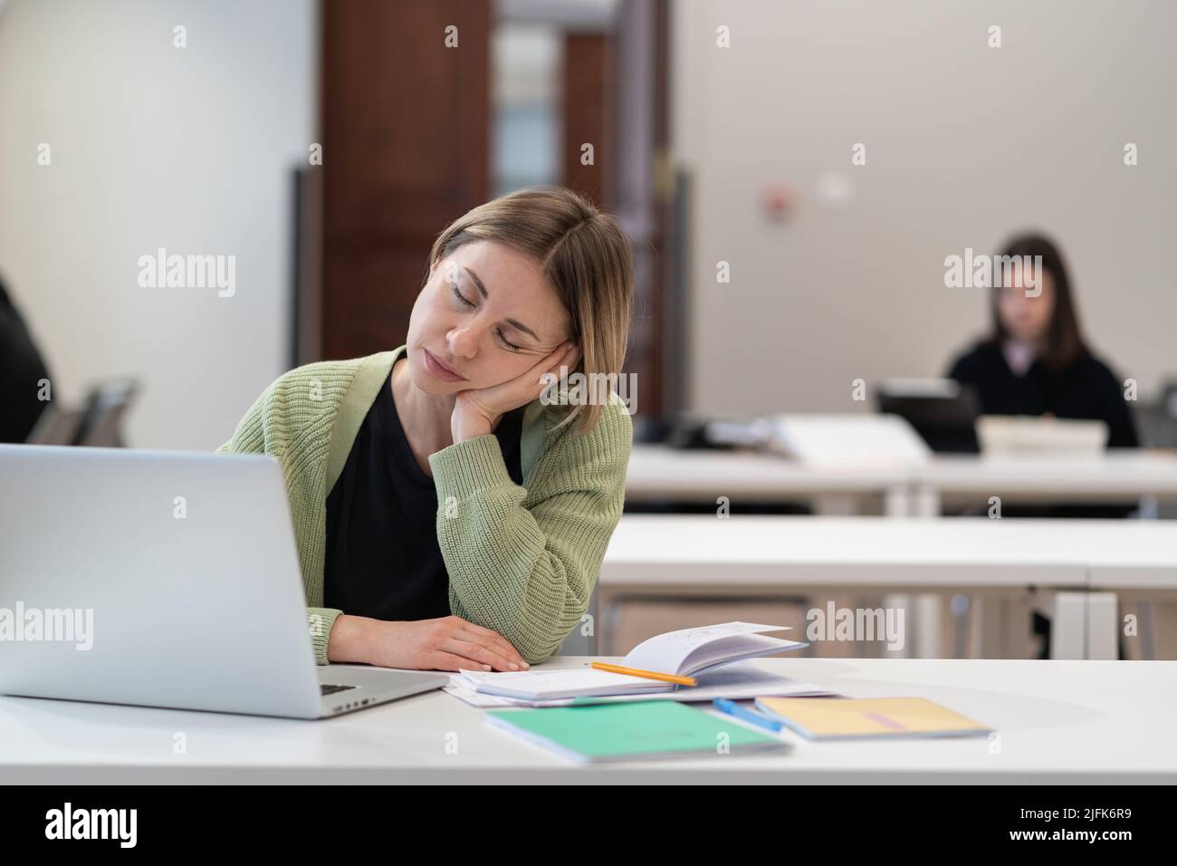 Exhausted mature female student falling asleep during online lesson, studying on laptop in ...