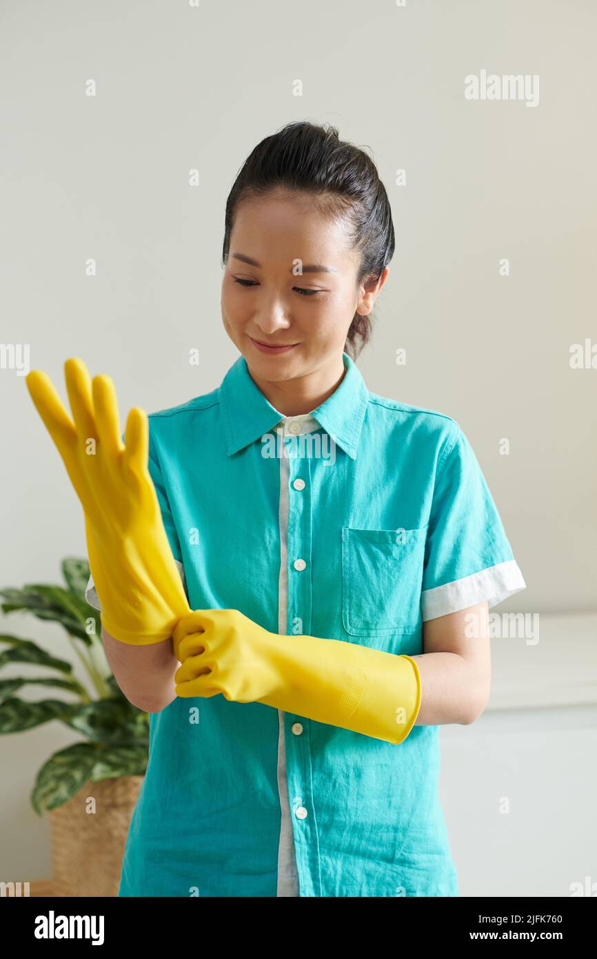 Asian young cleaner putting on uniform and rubber gloves ready to work ...