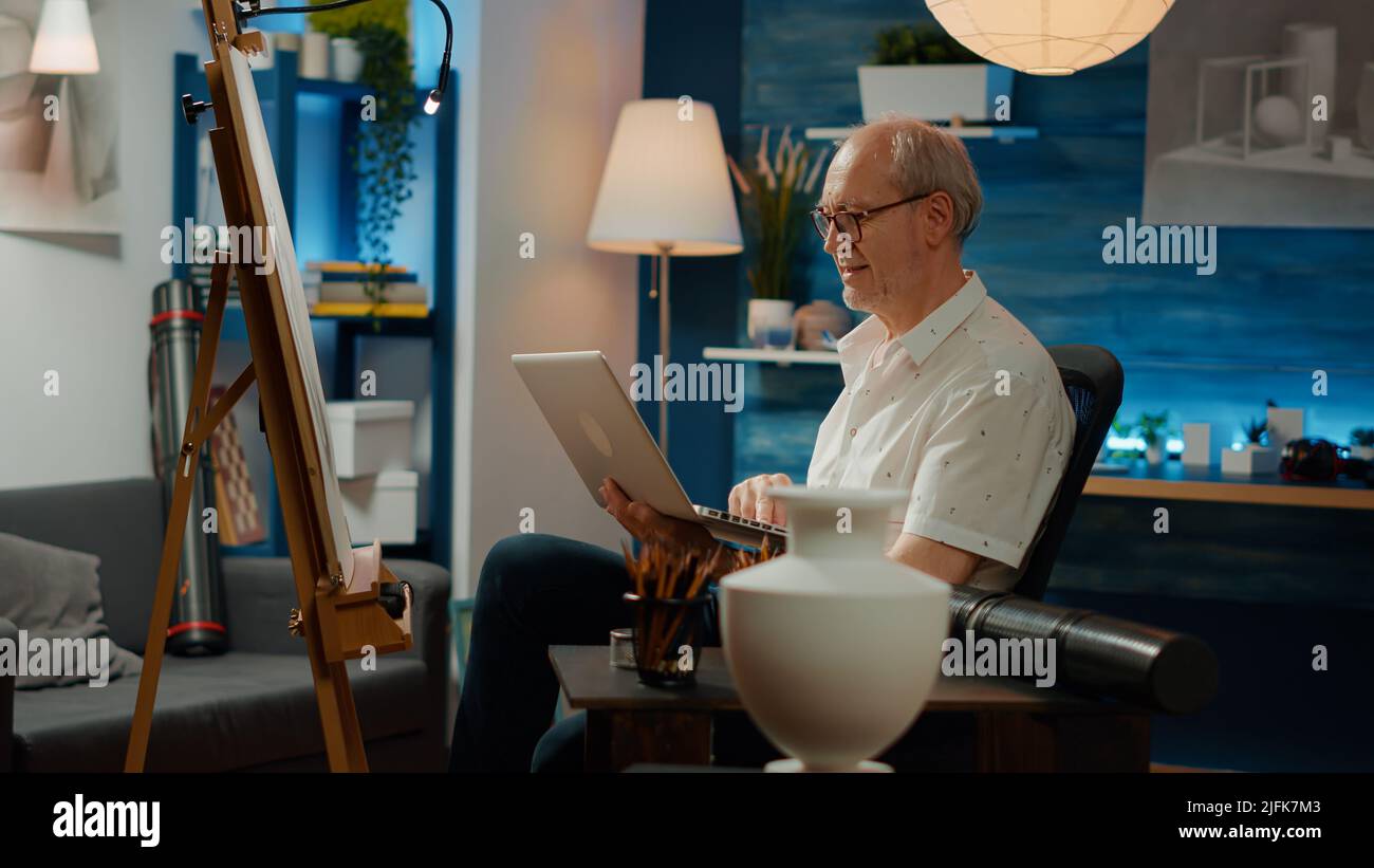 Old person looking at drawing inspiration online on laptop to create ...