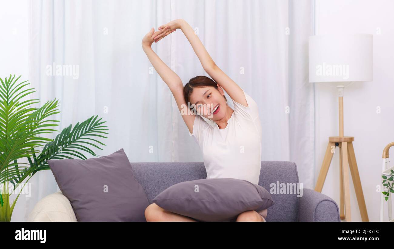 Lifestyle in living room concept, Asian woman sitting on couch to stretching for relaxation ...