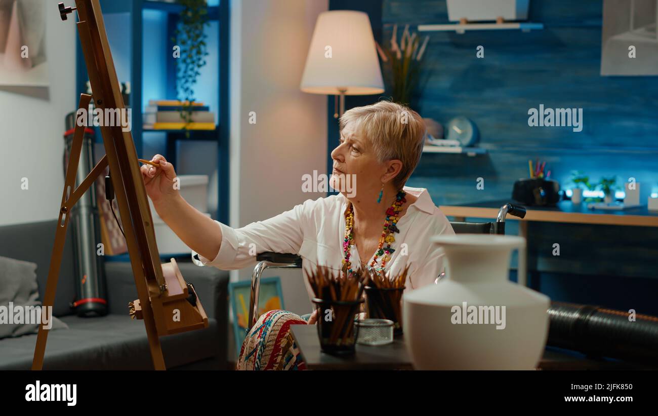 Senior artist with chronic impairment drawing vase design on canvas ...