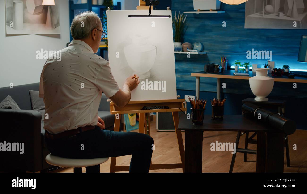Senior artist using pencils to draw artwork of vase model on white ...