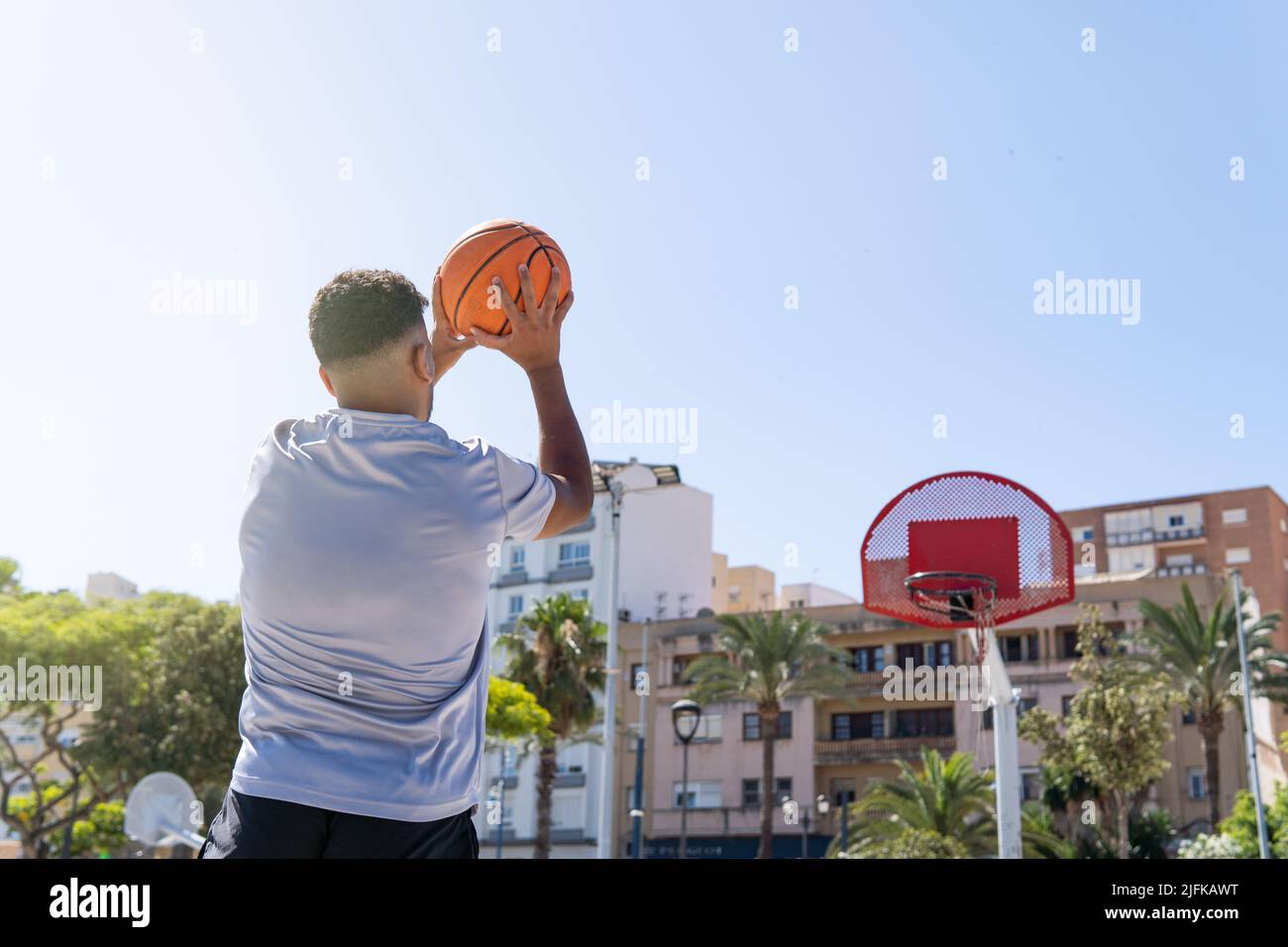 Rear view of a young muslim man throwing a basketball into a basket in ...