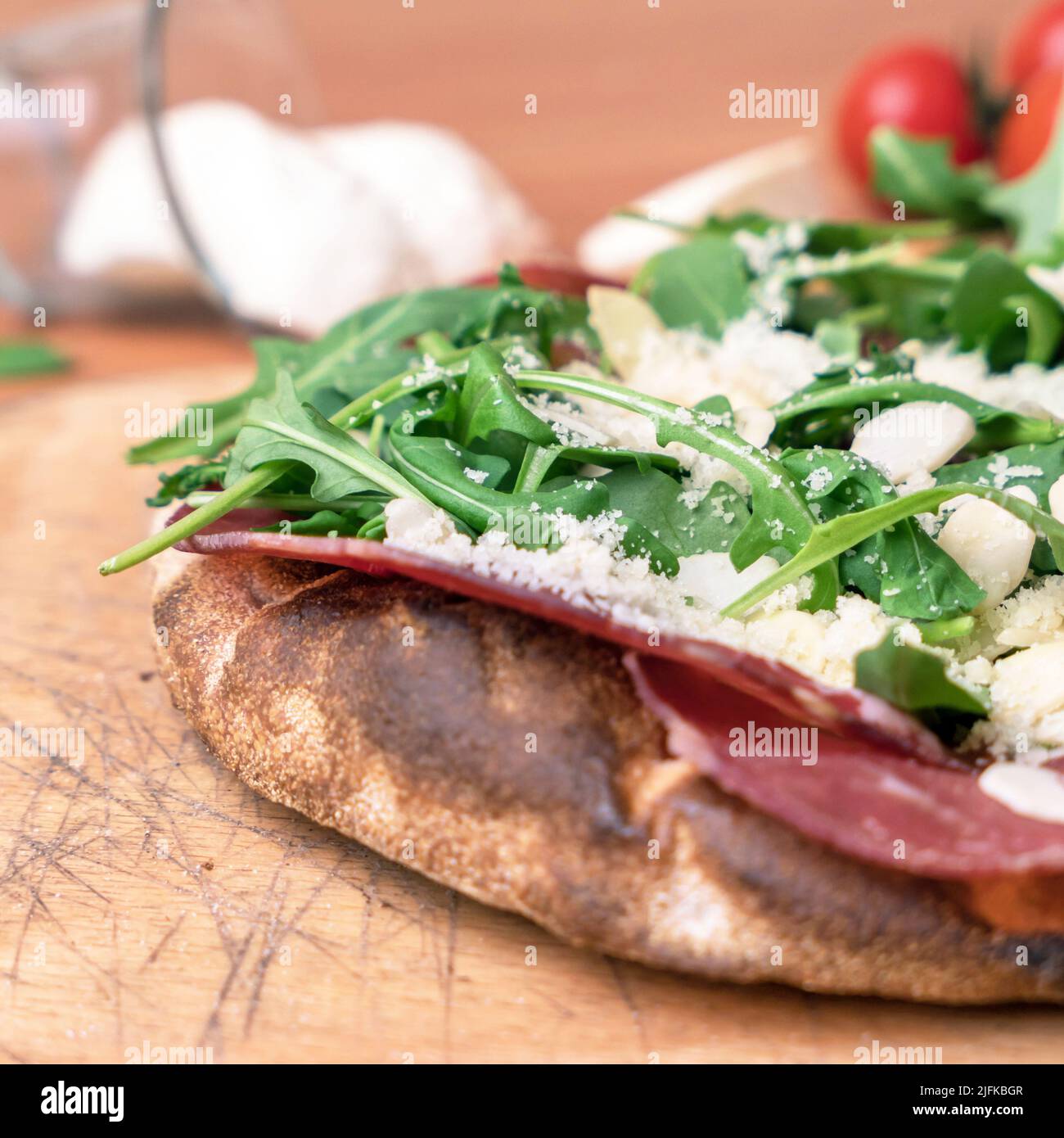 Close-up of a pizza with raw ham, parmesan cheese, almonds and rocket ...
