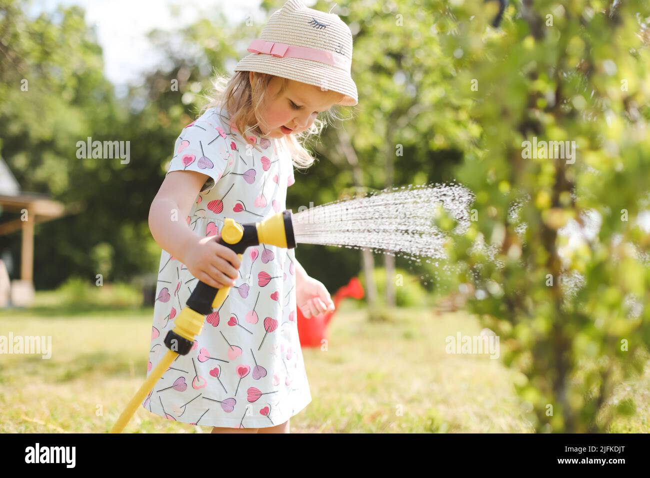 Adorable little girl playing with a garden hose on hot and sunny summer ...
