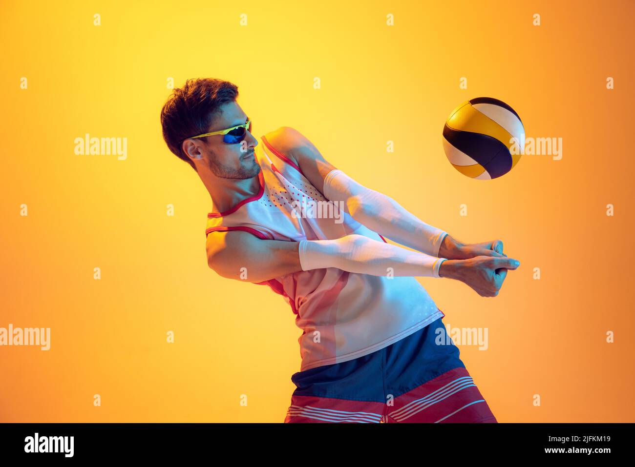 Portrait of young man, beach volleyball player in motion, bumping ball ...