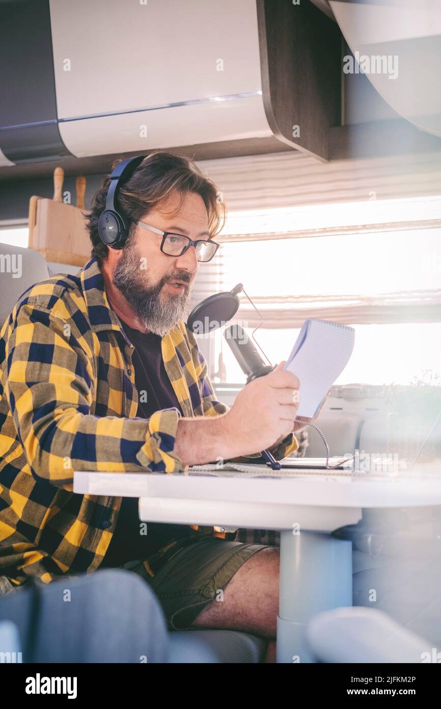 Modern adult man working with laptop and microphone inside a camper van ...