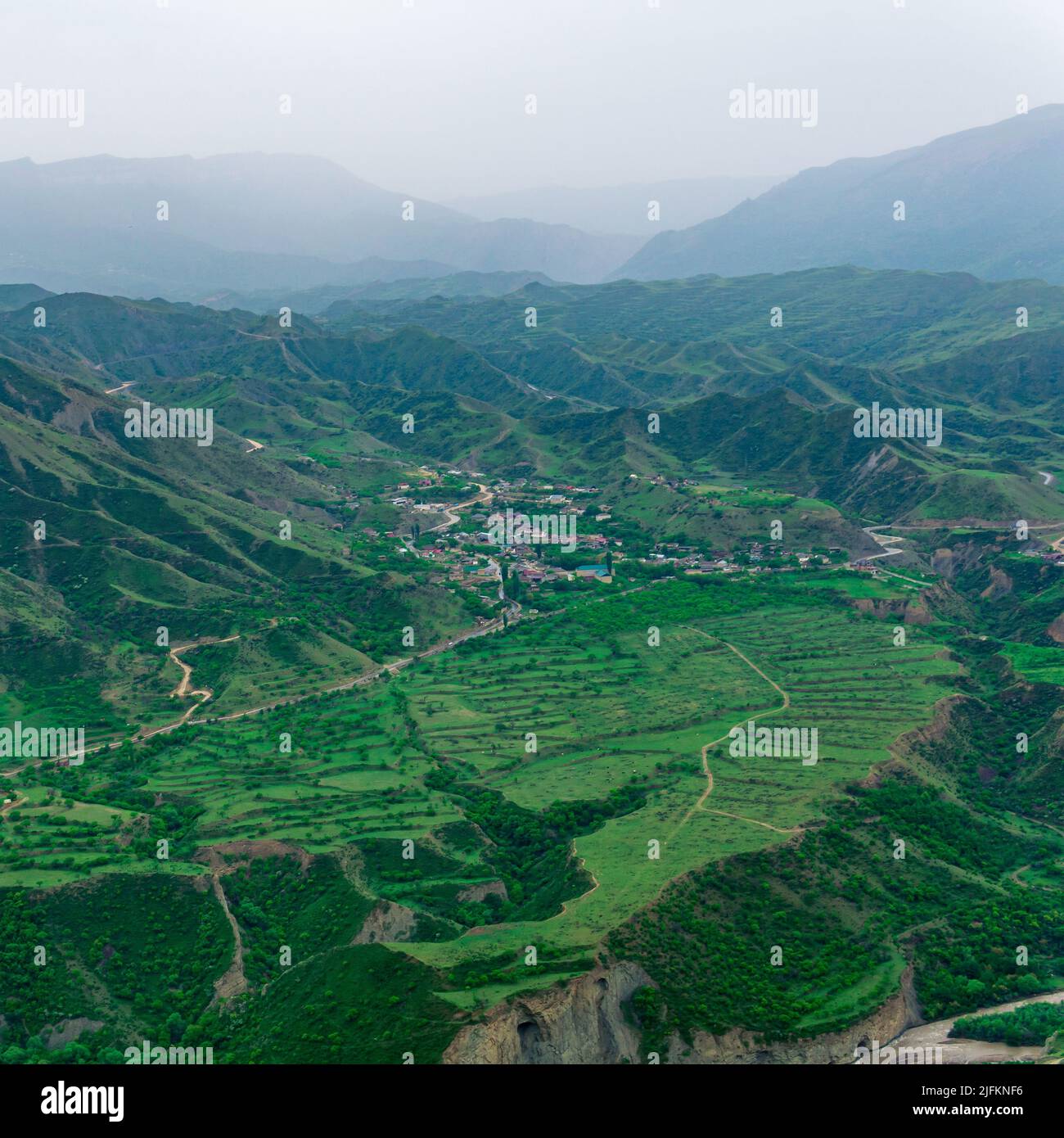 foggy highland valley with vliiage and fields between mountain peaks ...