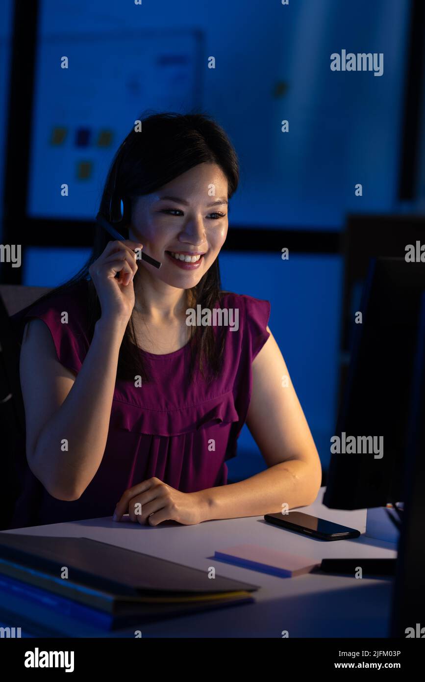 Asian female customer representative talking over headset and using ...