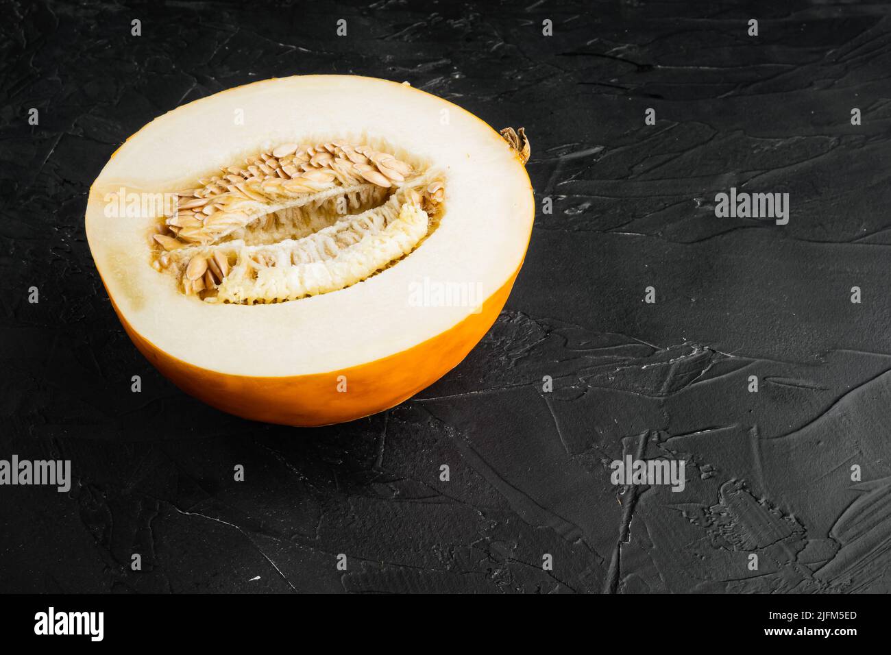 Ripe fresh yellow melon half, on black dark stone table background ...