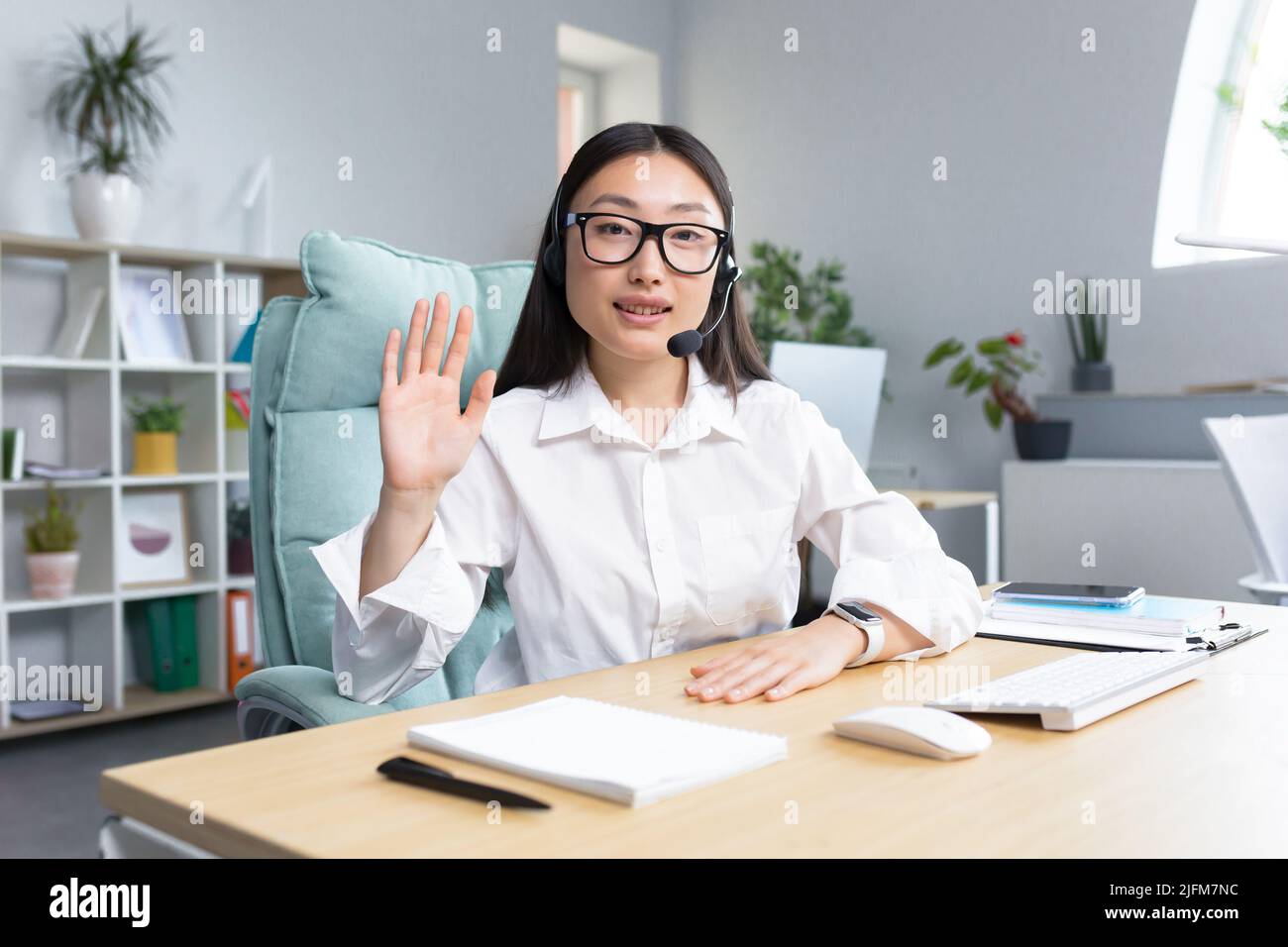 Young Asian call center worker looking at camera smiling waving ...