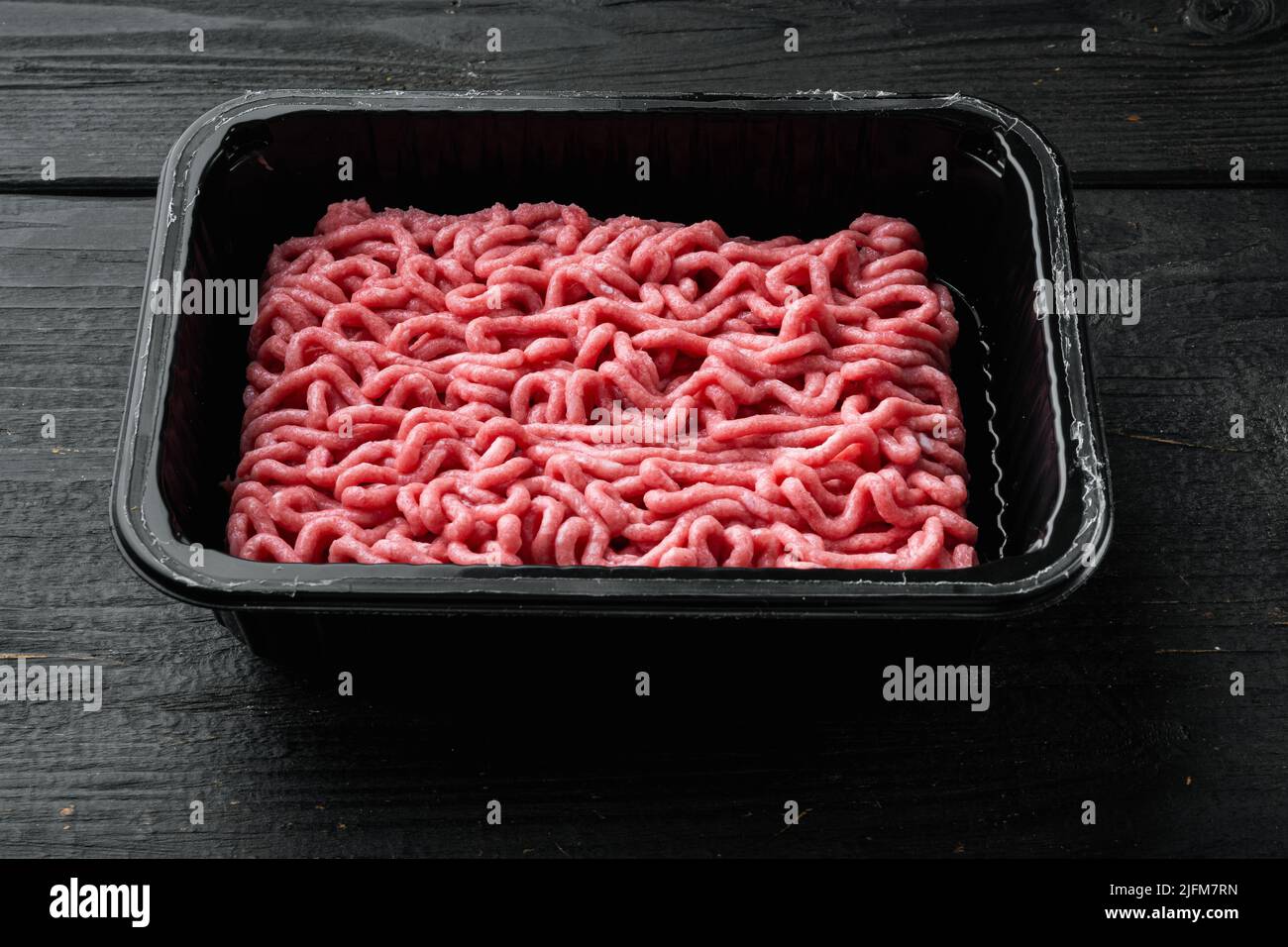 Fresh minced meat in plastic box packaging tray, on black wooden table ...