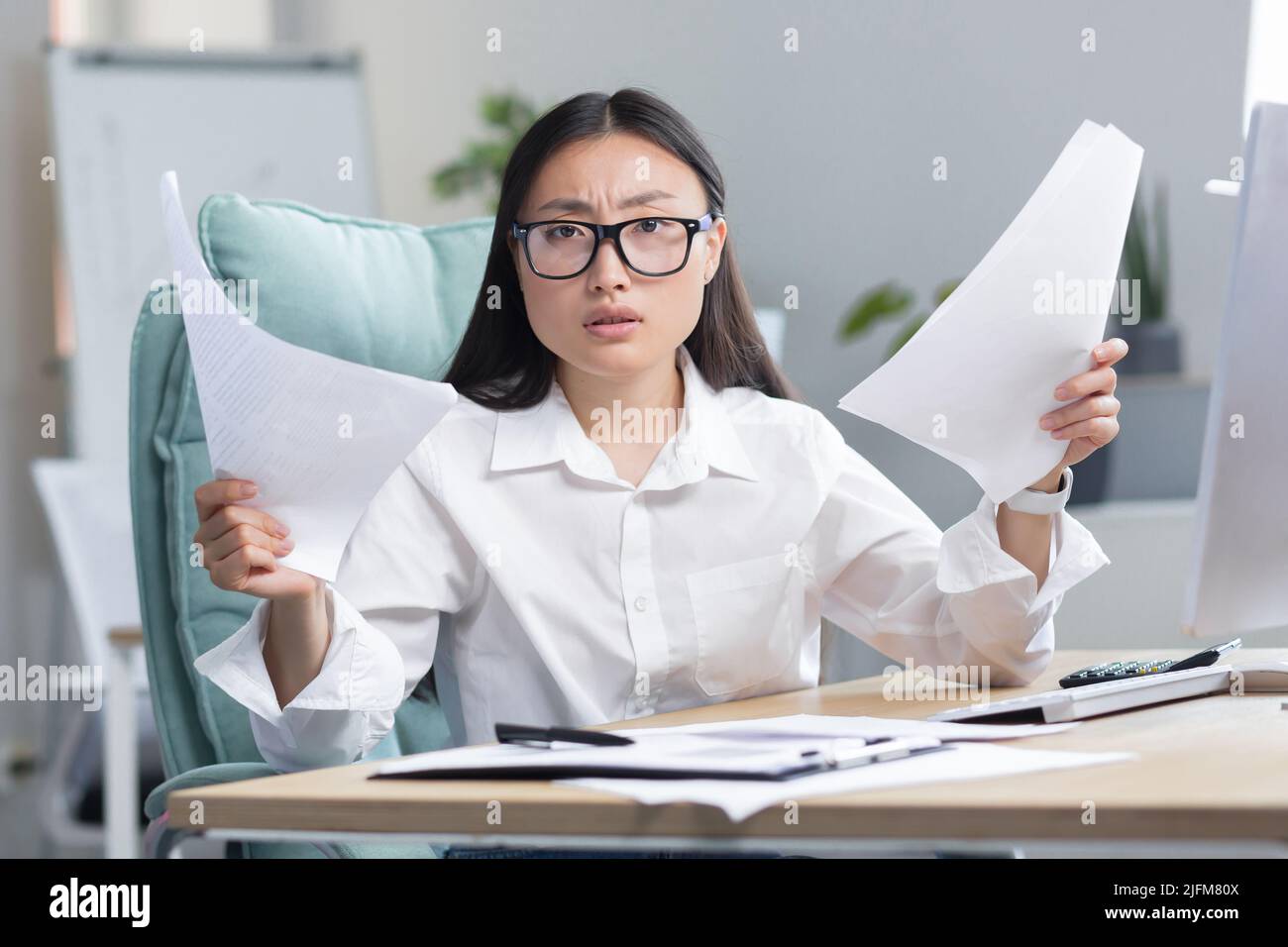 Frustrated and upset asian business woman working in office, holding ...