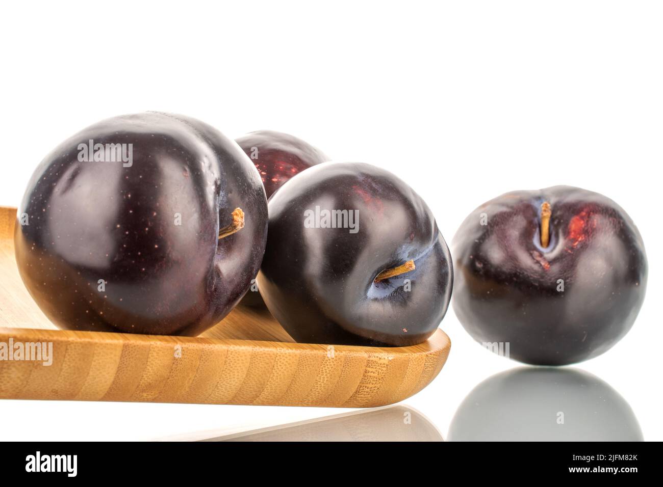 Four dark blue organic plums on a wooden tray, close-up, isolated on ...