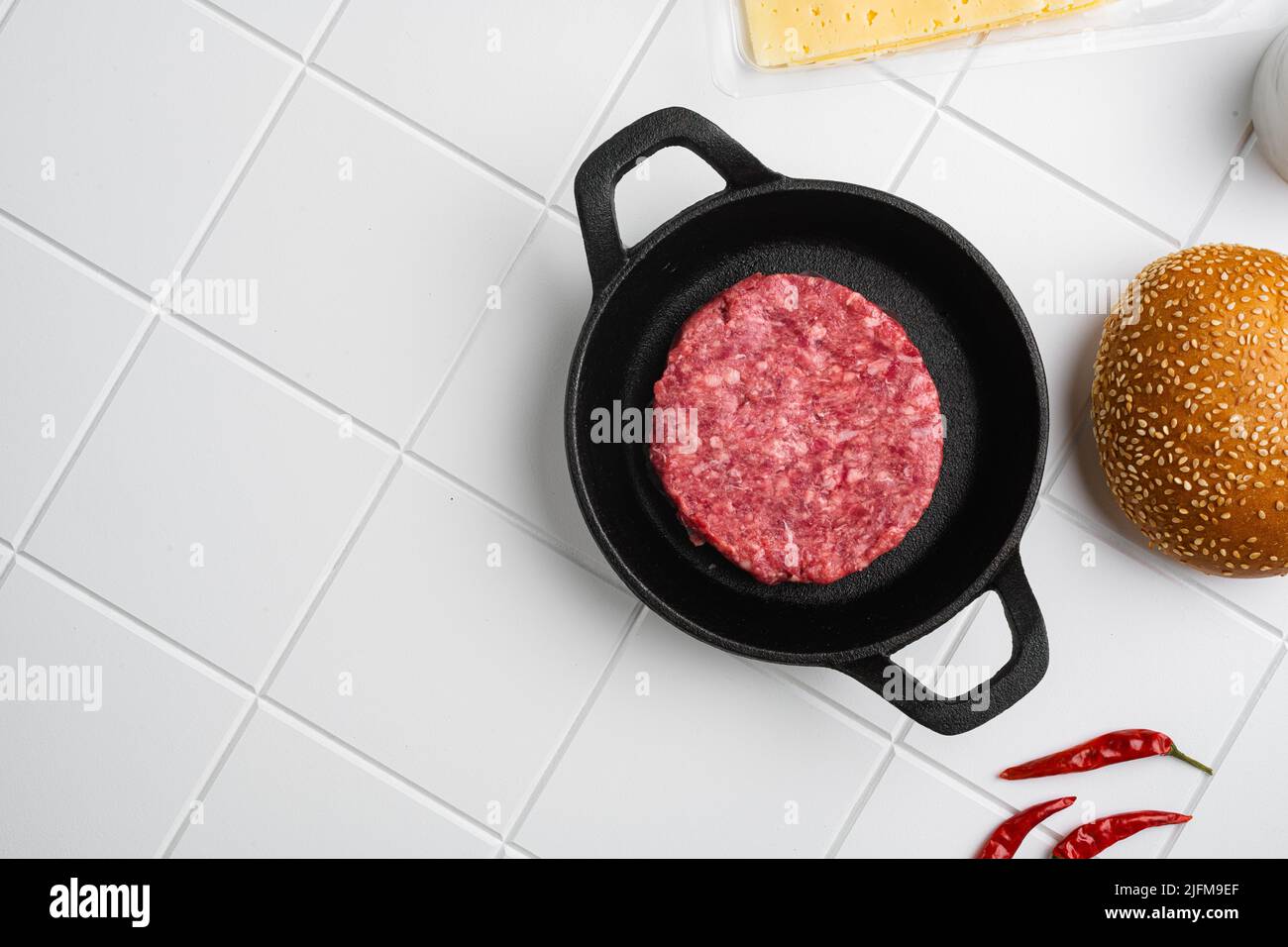 Raw fresh large beef burger on white ceramic squared tile table ...
