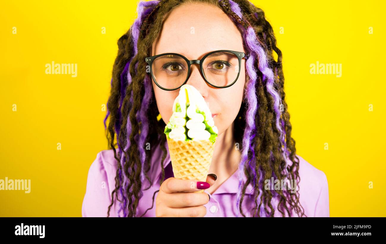 Young beautiful woman in glasses with at ice cream, yellow background ...