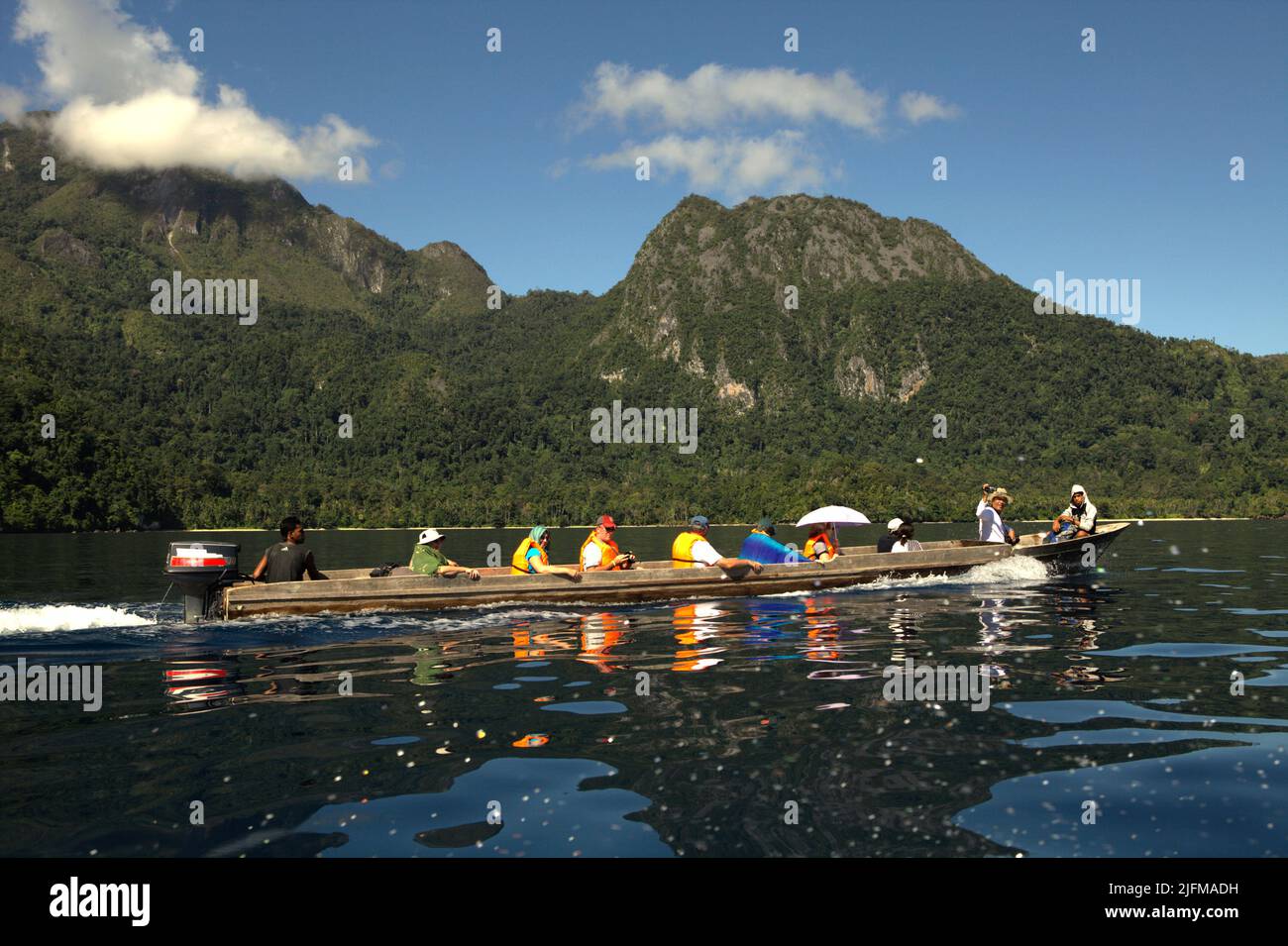 A boat carrying tourists is sailing on sea water in a background of the ...