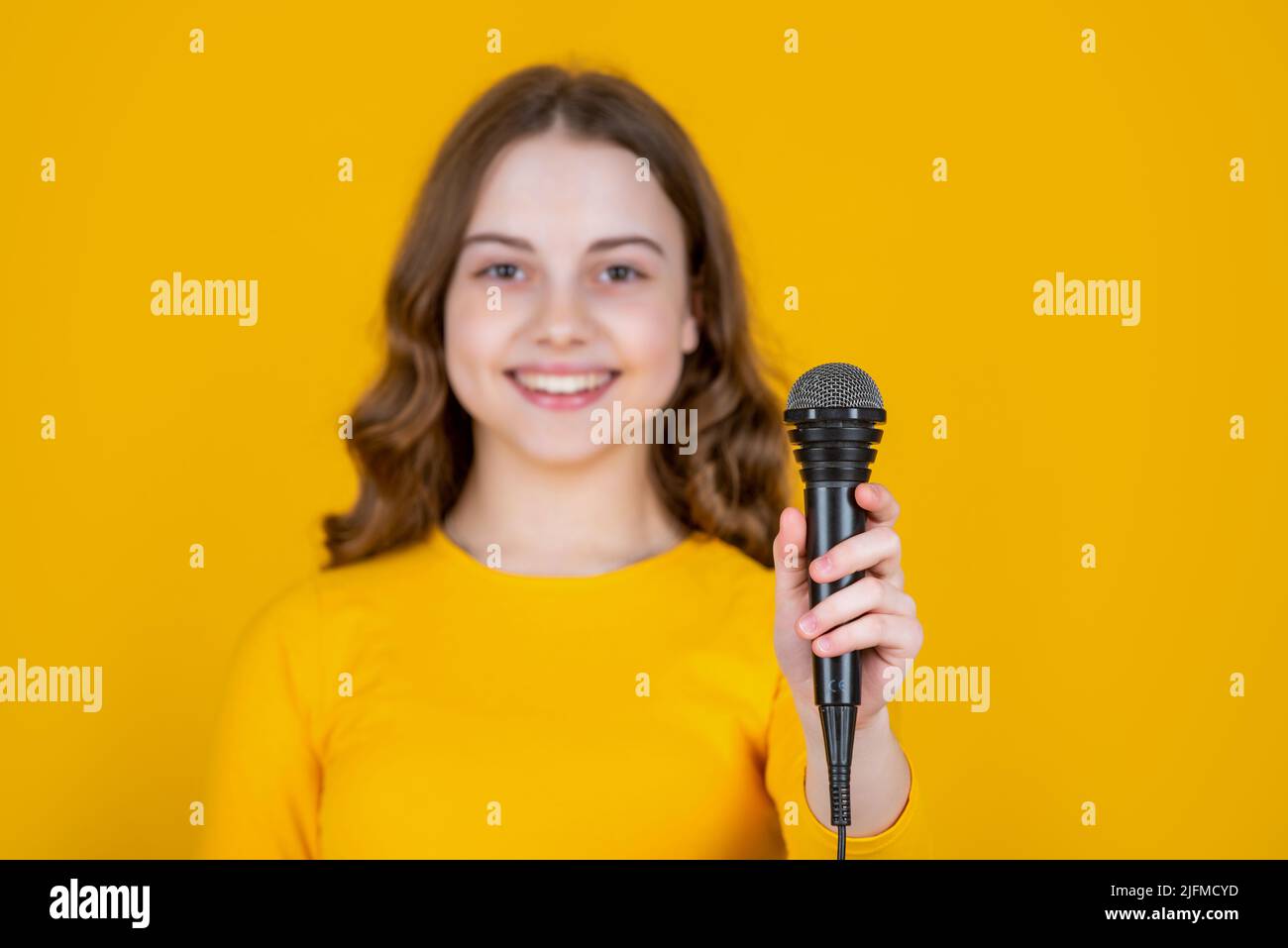 microphone in hand of teen girl on yellow background. selective focus ...