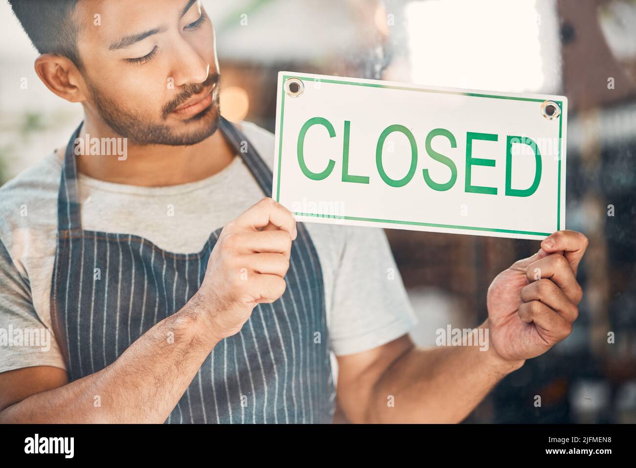One young hispanic man holding a closed sign at a window on display in ...