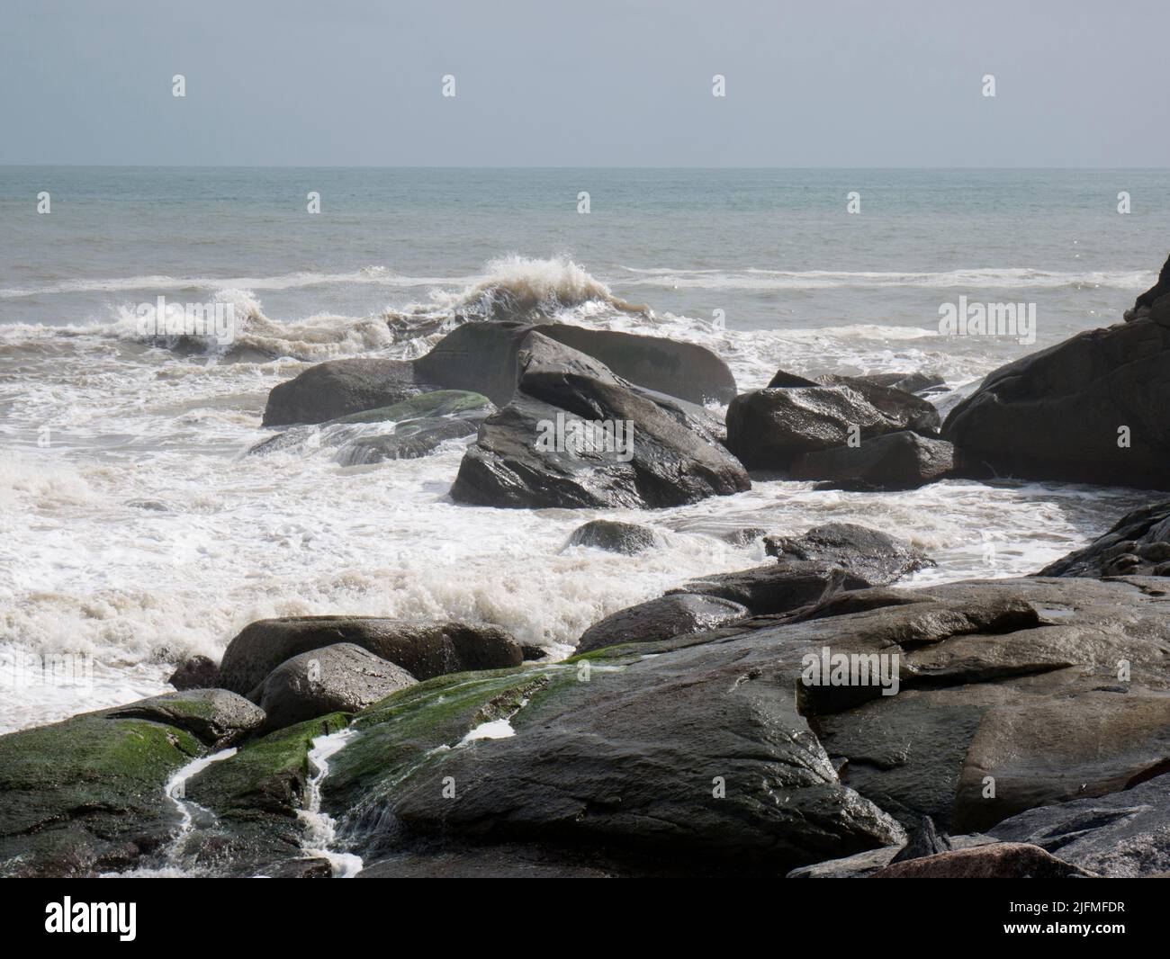 Rocky seashore with waves hitting creating foam and splashing at ...