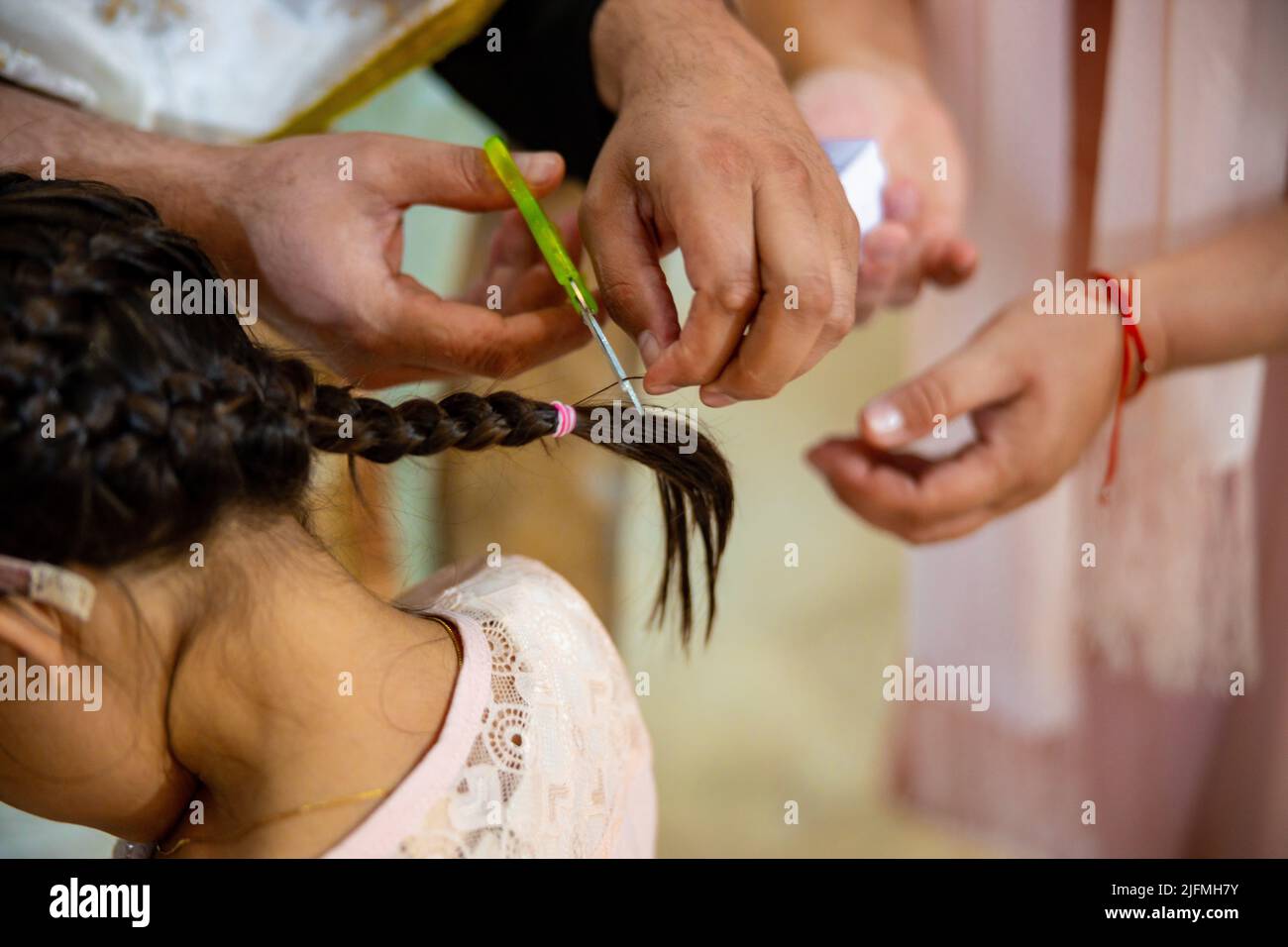 A priest cutting a little girl's hair for her baptism ceremony ...