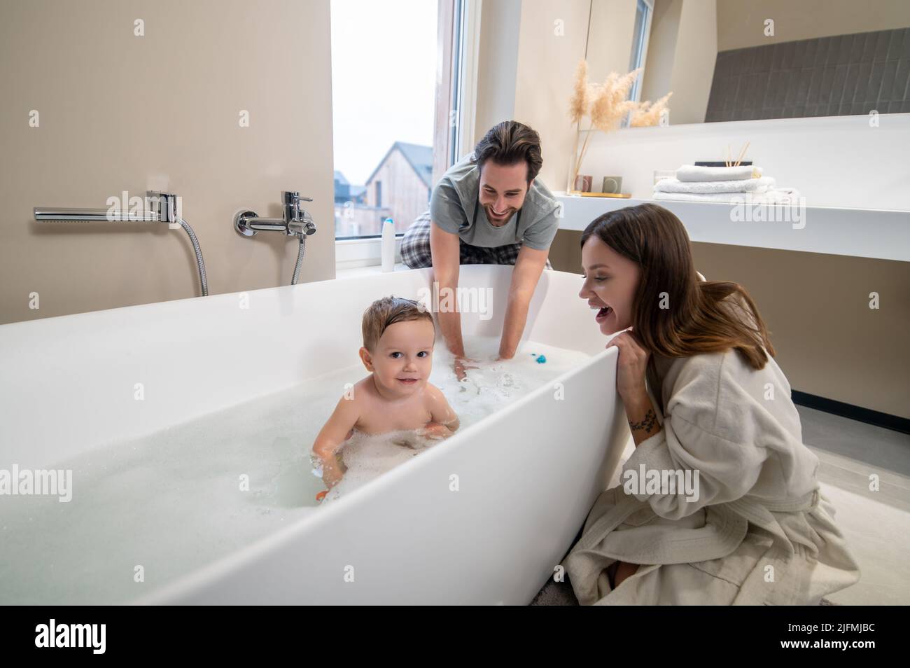Child looking at camera in bathtub and parents watching Stock Photo - Alamy