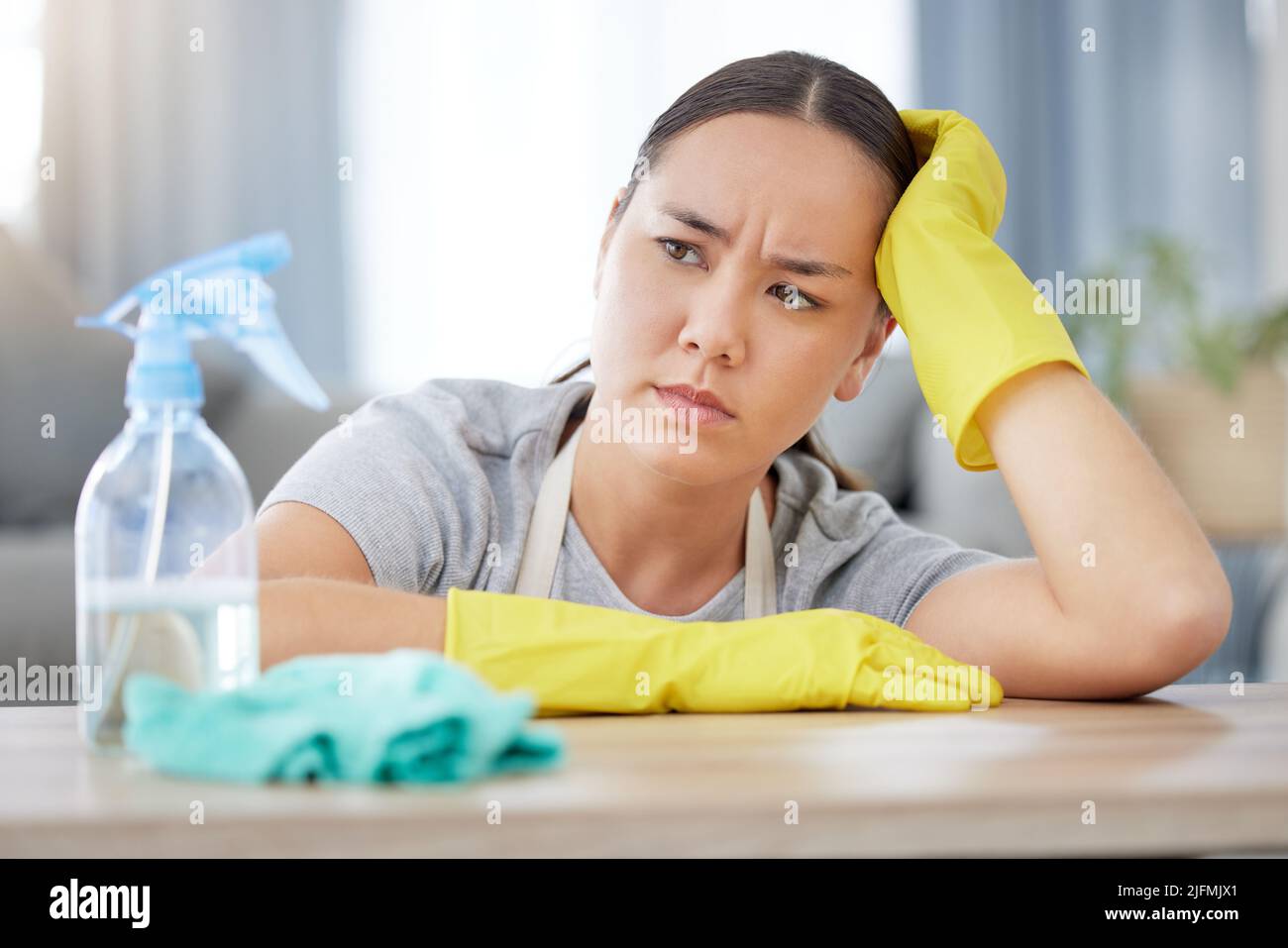 A mixed race domestic worker looking depressed while cleaning. One ...