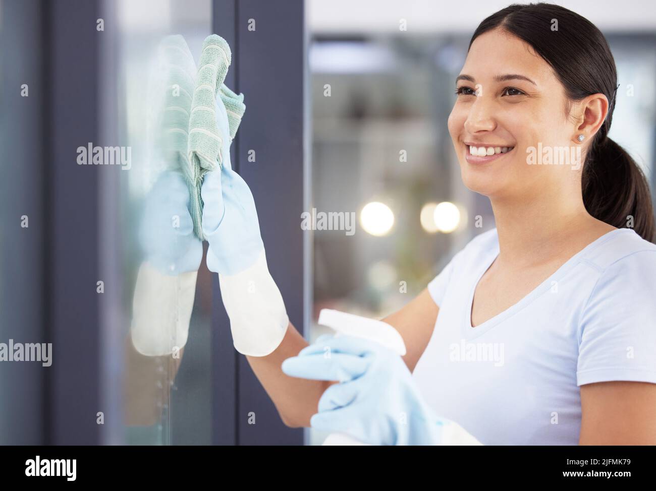 A young happy mixed race domestic worker using a cloth on a window. One ...