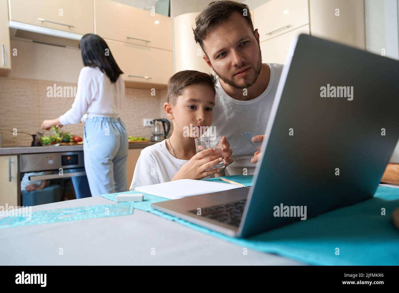 Boy drinking water while father explaining him lesson on laptop Stock ...