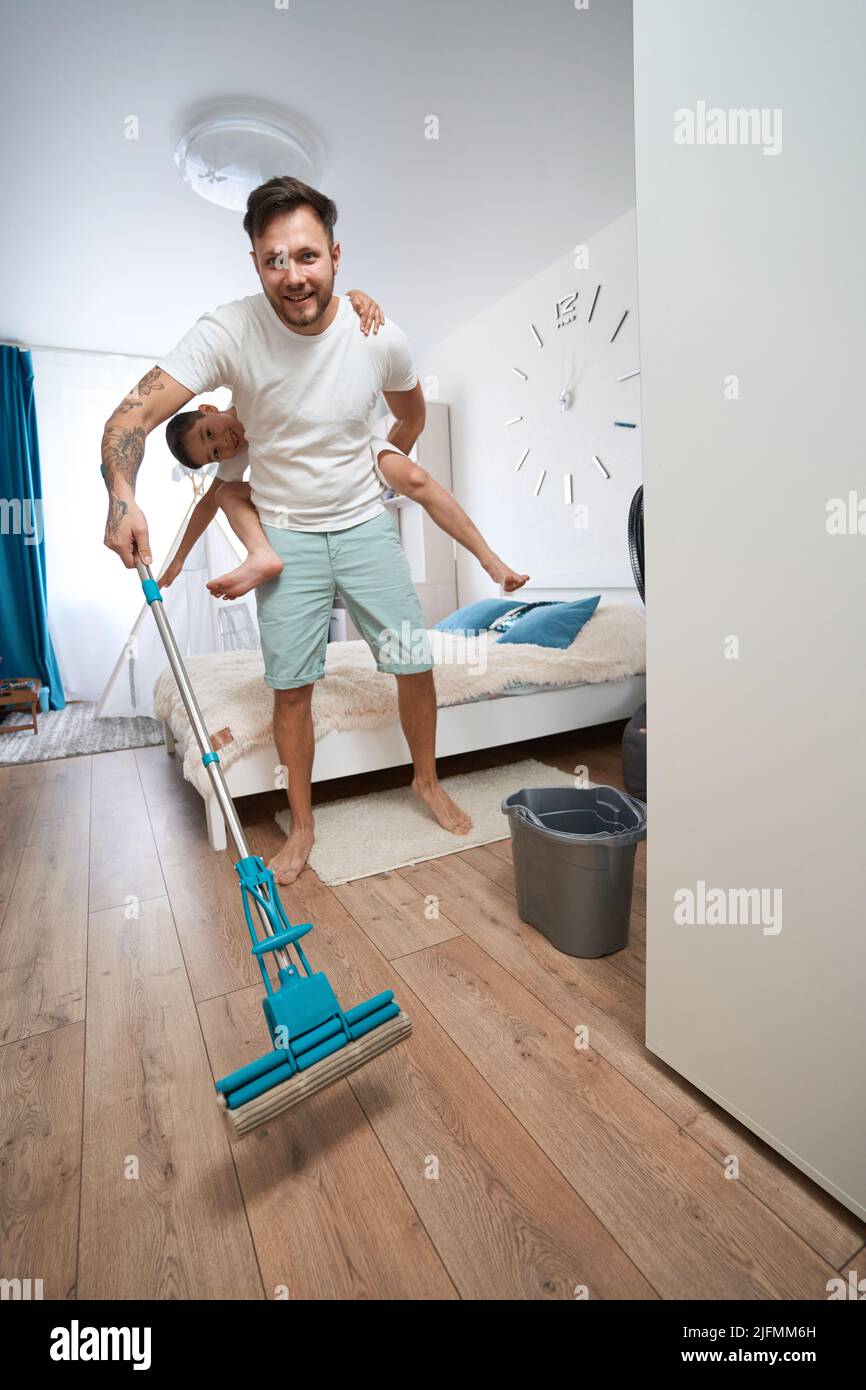 Boy clinging to man back while washing floor with mop Stock Photo - Alamy