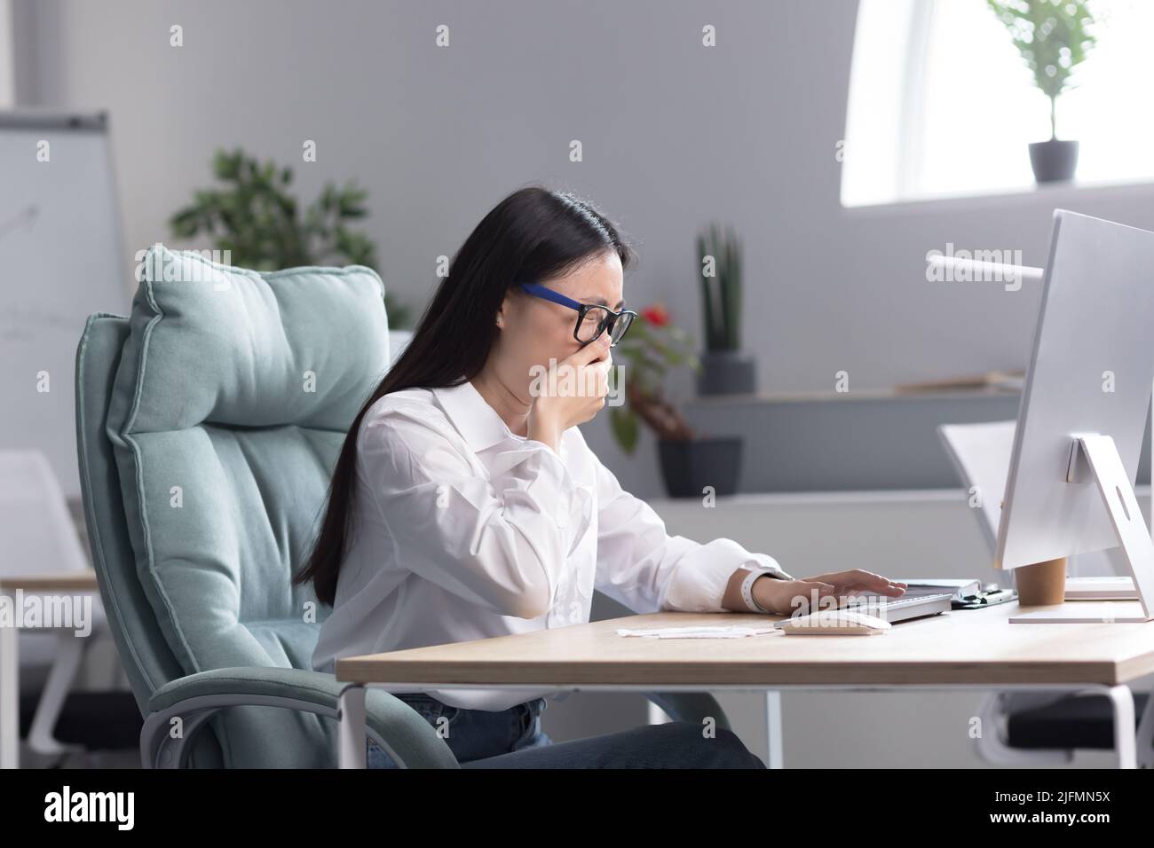 Sick Asian female office worker, has cold and flu, coughs and sneezes ...