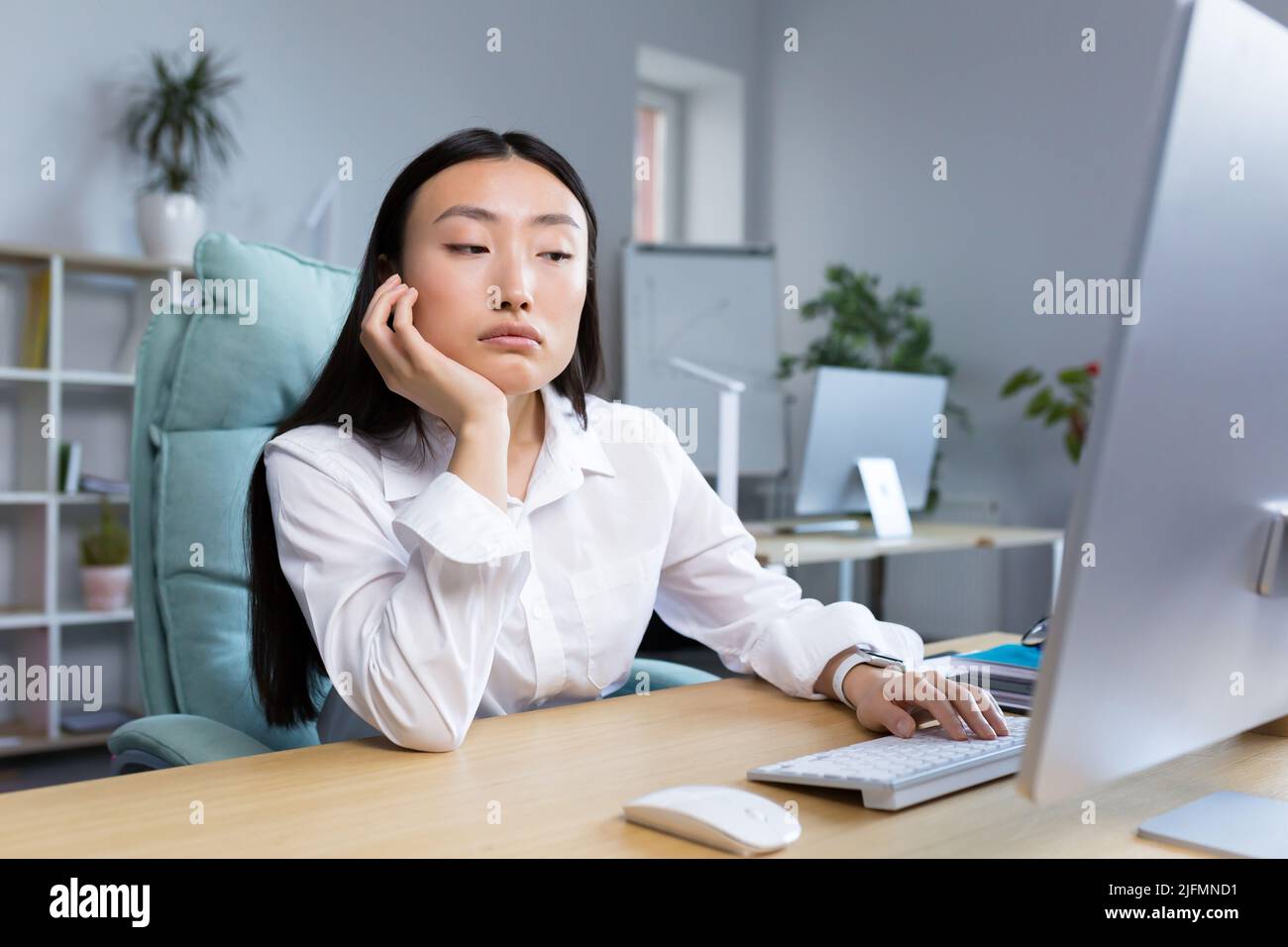 A sad business woman works in a modern office, an Asian woman thinks ...