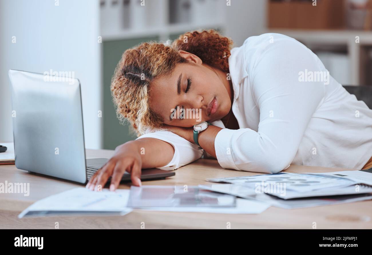 Young mixed race businesswoman sleeping at her desk in an office alone ...