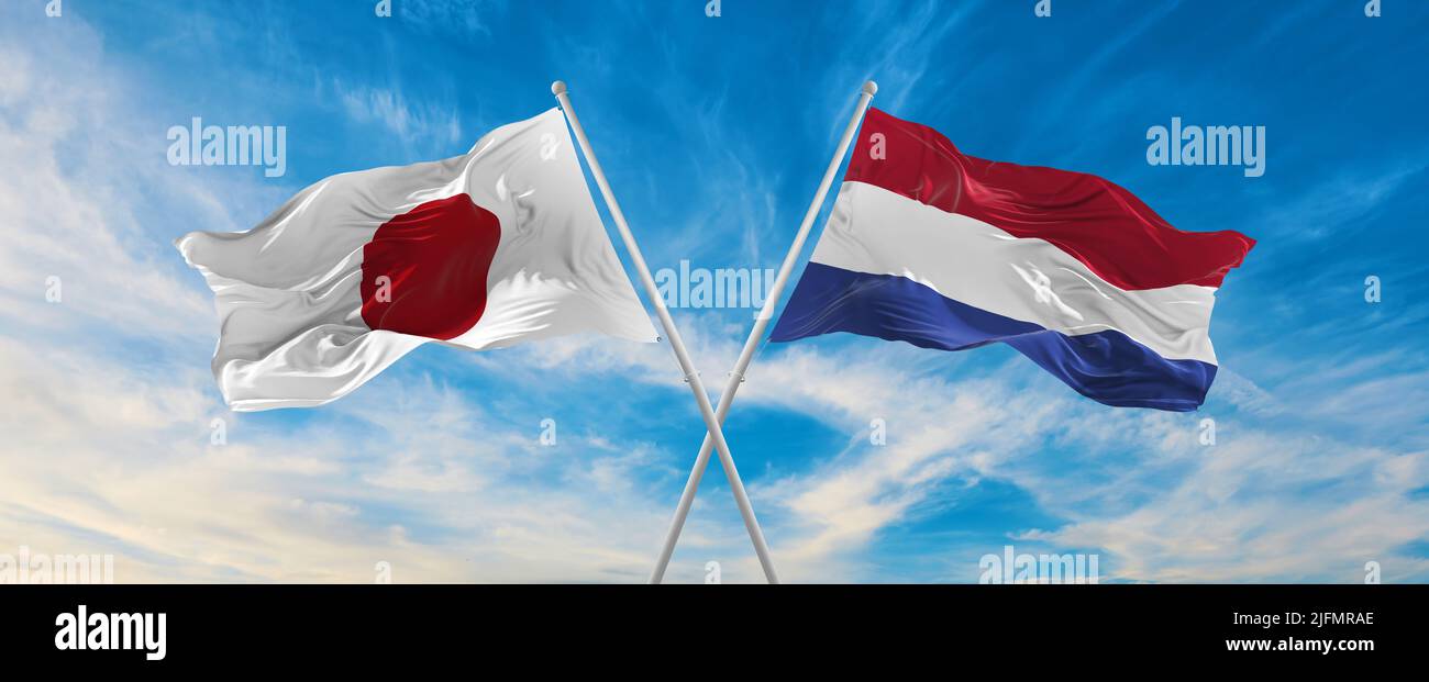 two crossed flags japan and Netherland waving in wind at cloudy sky ...