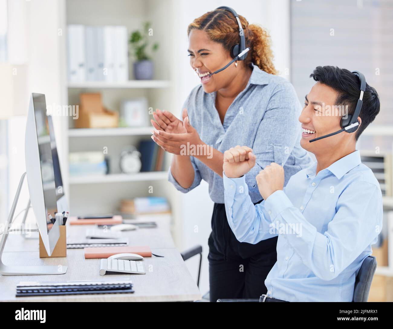 Two happy young diverse call centre telemarketing agents clapping and ...