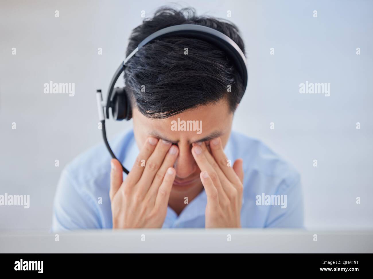 Stressed young asian male call centre agent getting a headache while ...