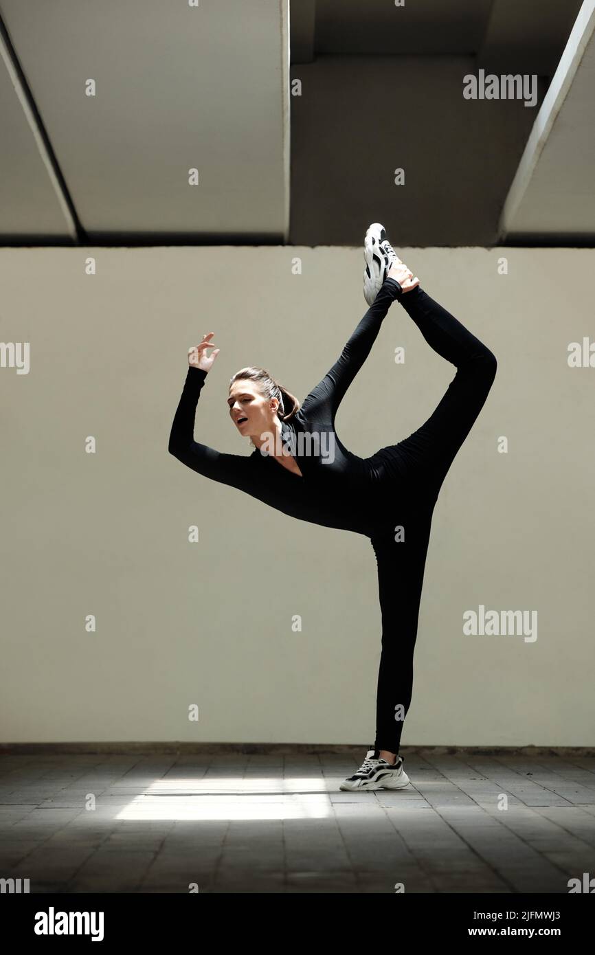 Young dancer girl in black suit doing stretching exercises raising her ...