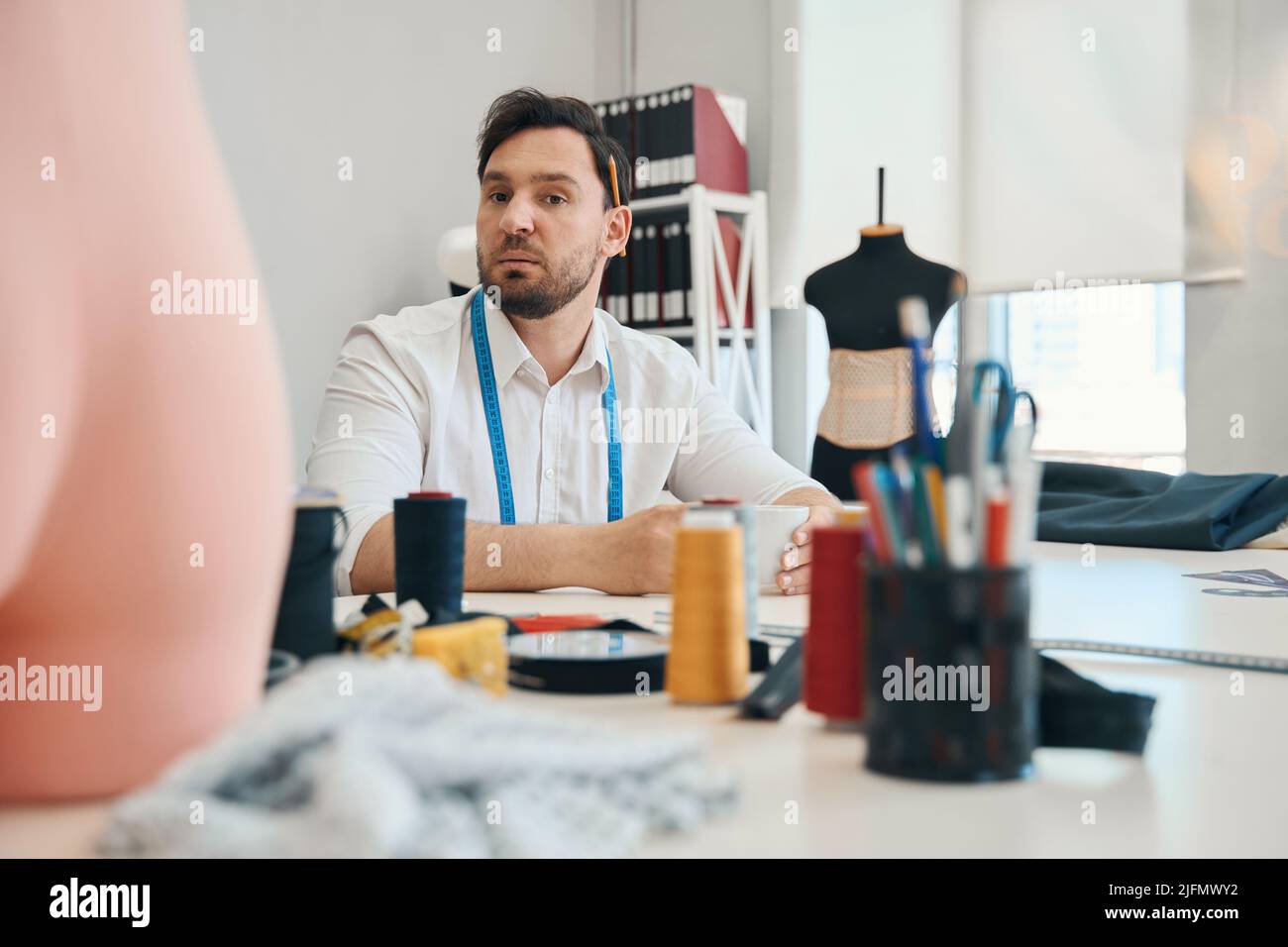 Couturier with length measuring tape around neck works in sewing ...