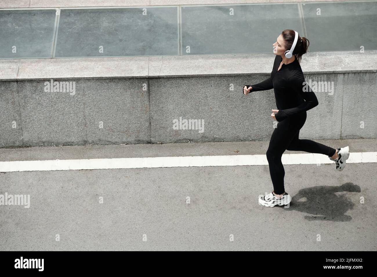 Young female athlete listening to music in headphones while running in ...