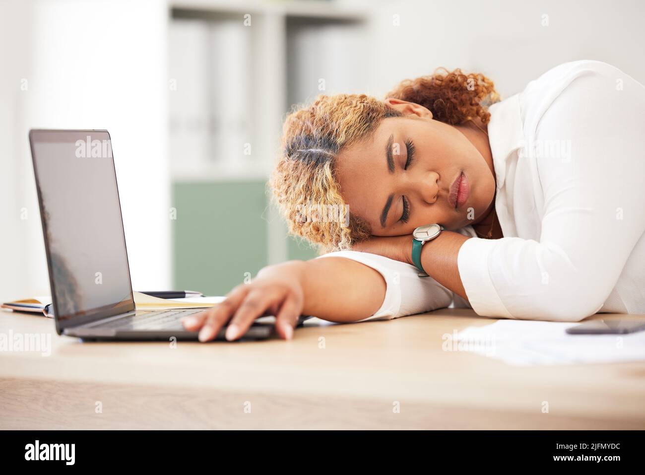 Young Mixed race businesswoman sleeping in a office in front of a laptop on the desk. Latin ...