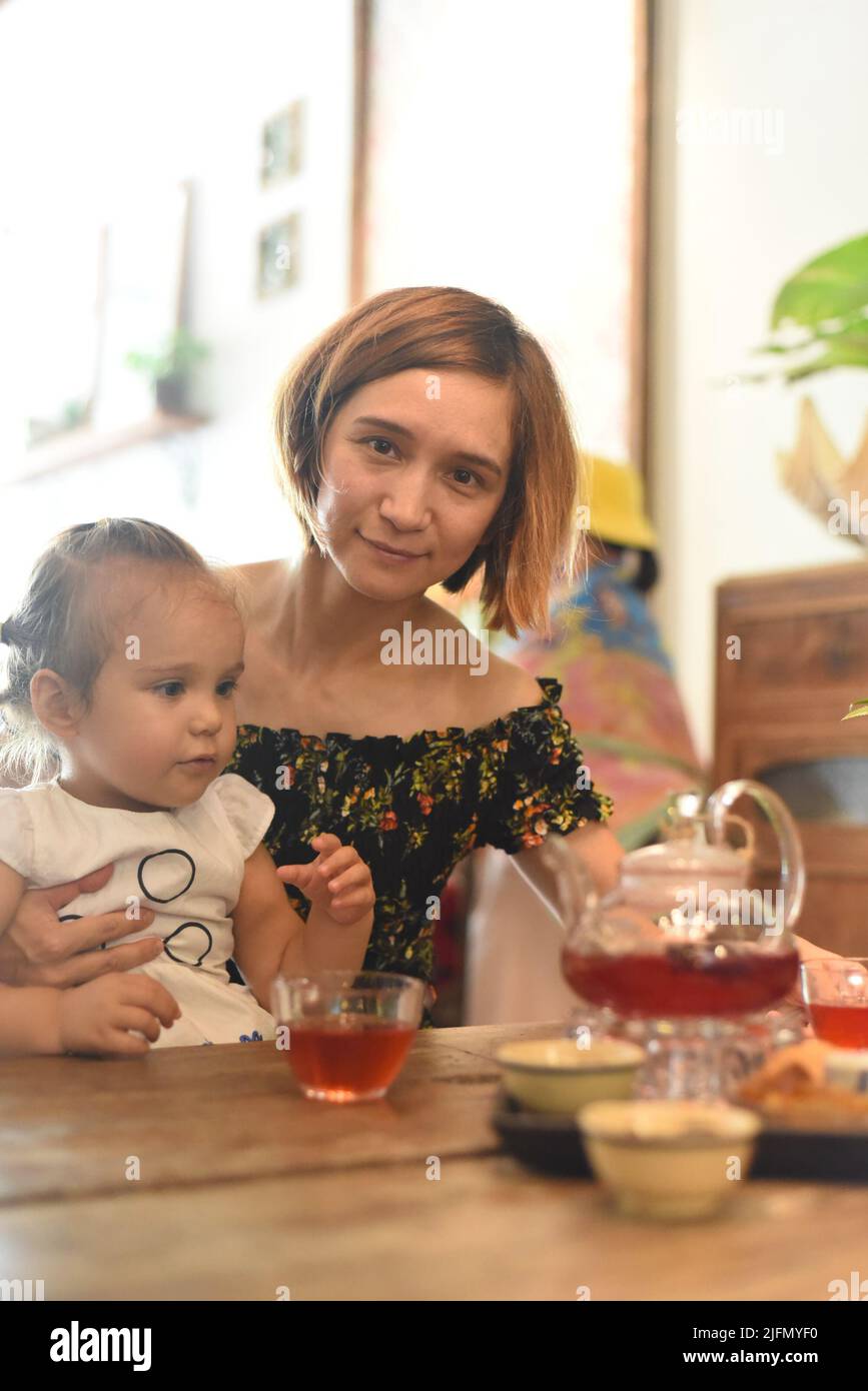 Young woman with a baby girl drinking tea from a tea pot in a coffee ...