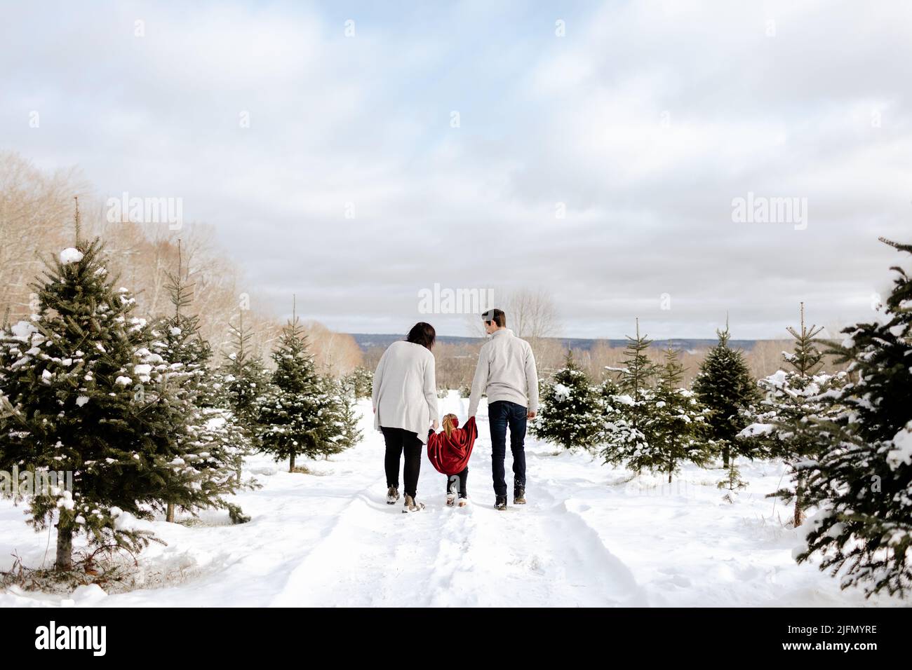A back shot of a family with daughter holding hands on white ice floor ...
