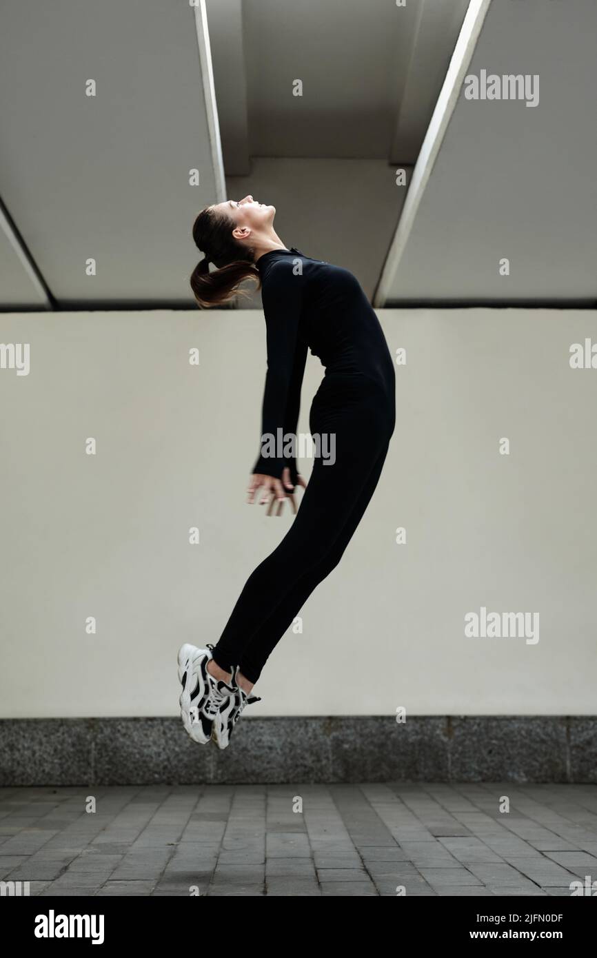 Young female dancer in black costume jumping during her modern dance ...