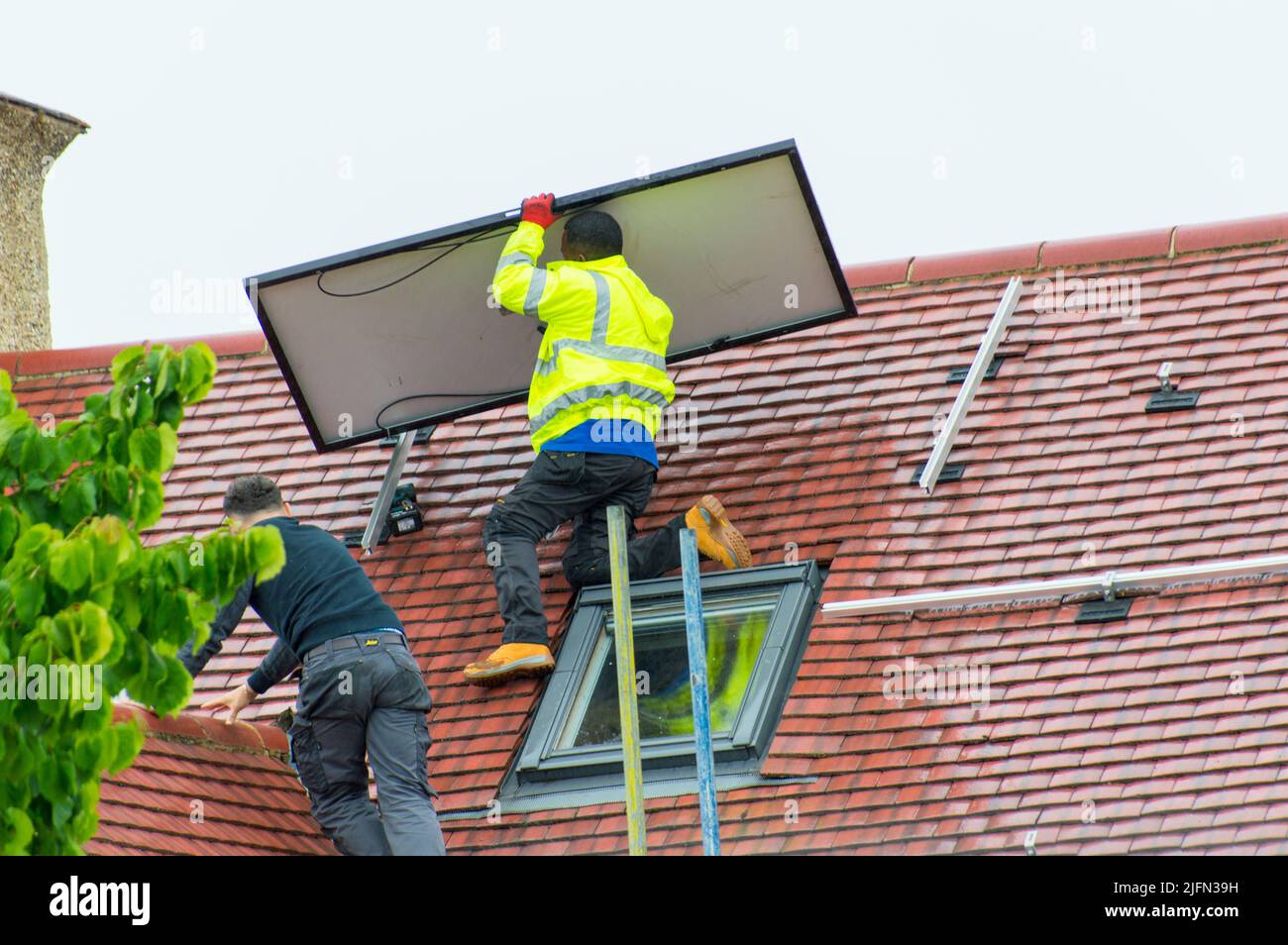 Two workman moving a solar panel to the roof to install Stock Photo - Alamy