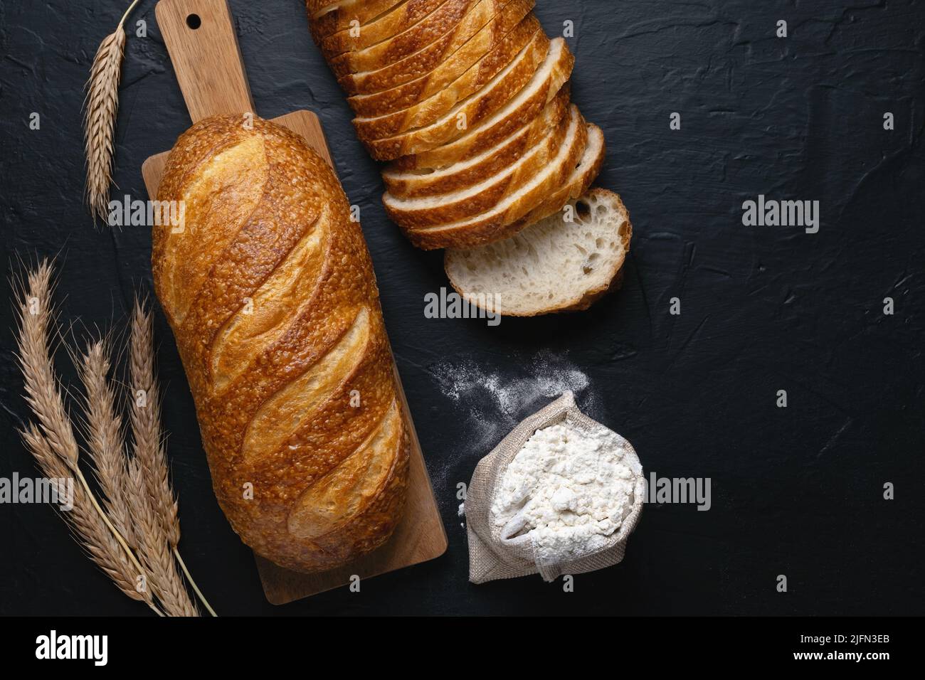 Fresh wheaten baton bread and flour on dark background.Top view. Copy ...