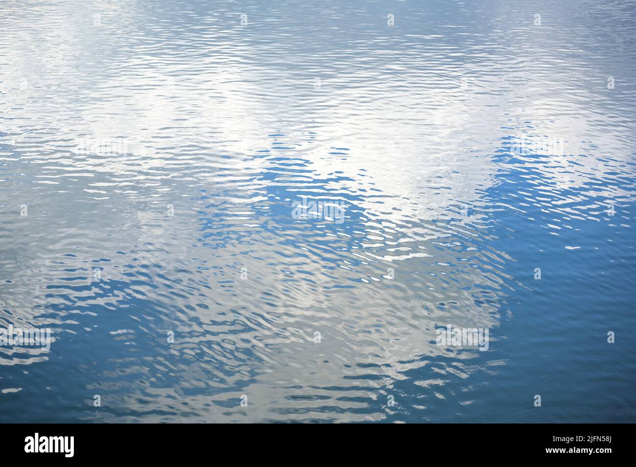 Blue gray water surface with very small waves and reflection of the ...