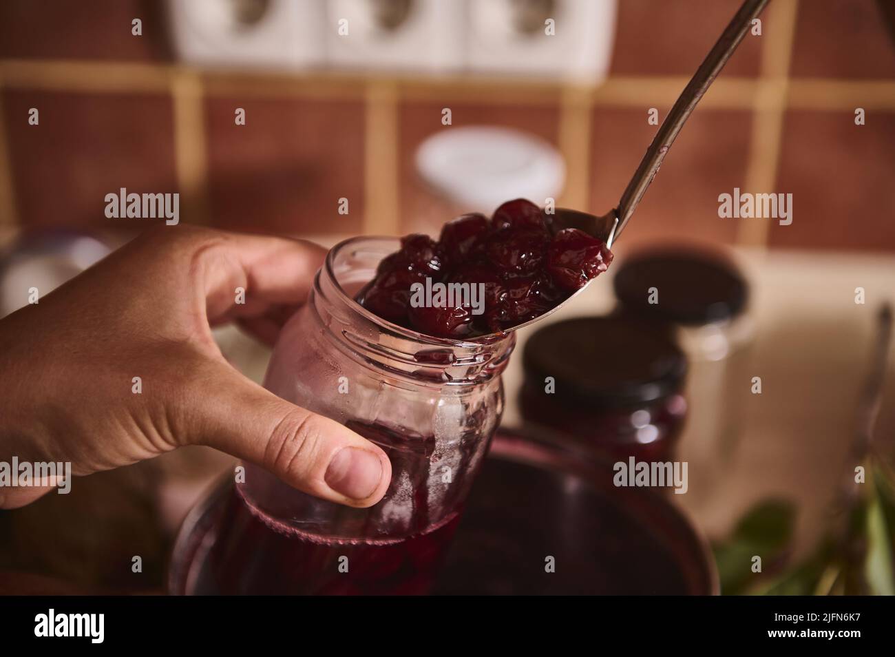 Close-up confectioner's hands holding kitchen spoon with cherry berries ...